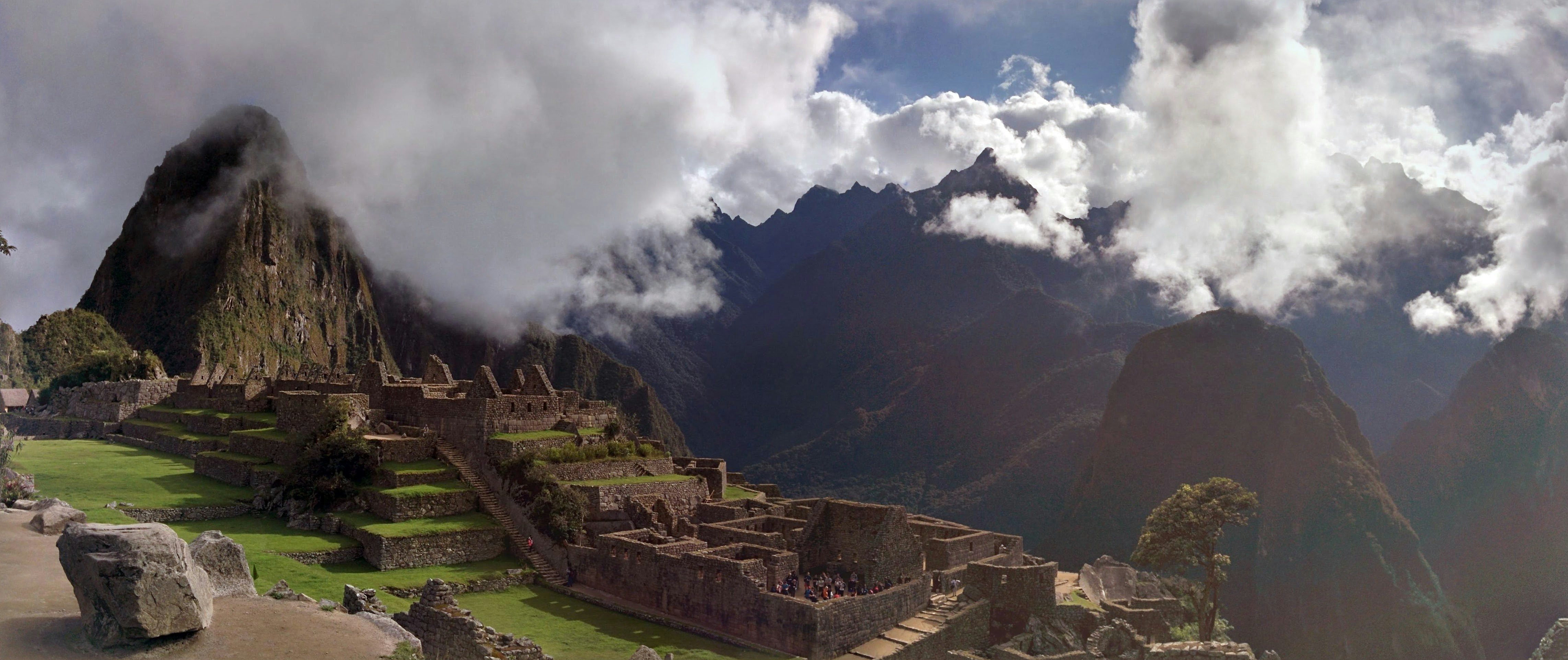 Machu Picchu&#x27;s intricate stone structures rise amidst dramatic mountain scenery and swirling clouds.