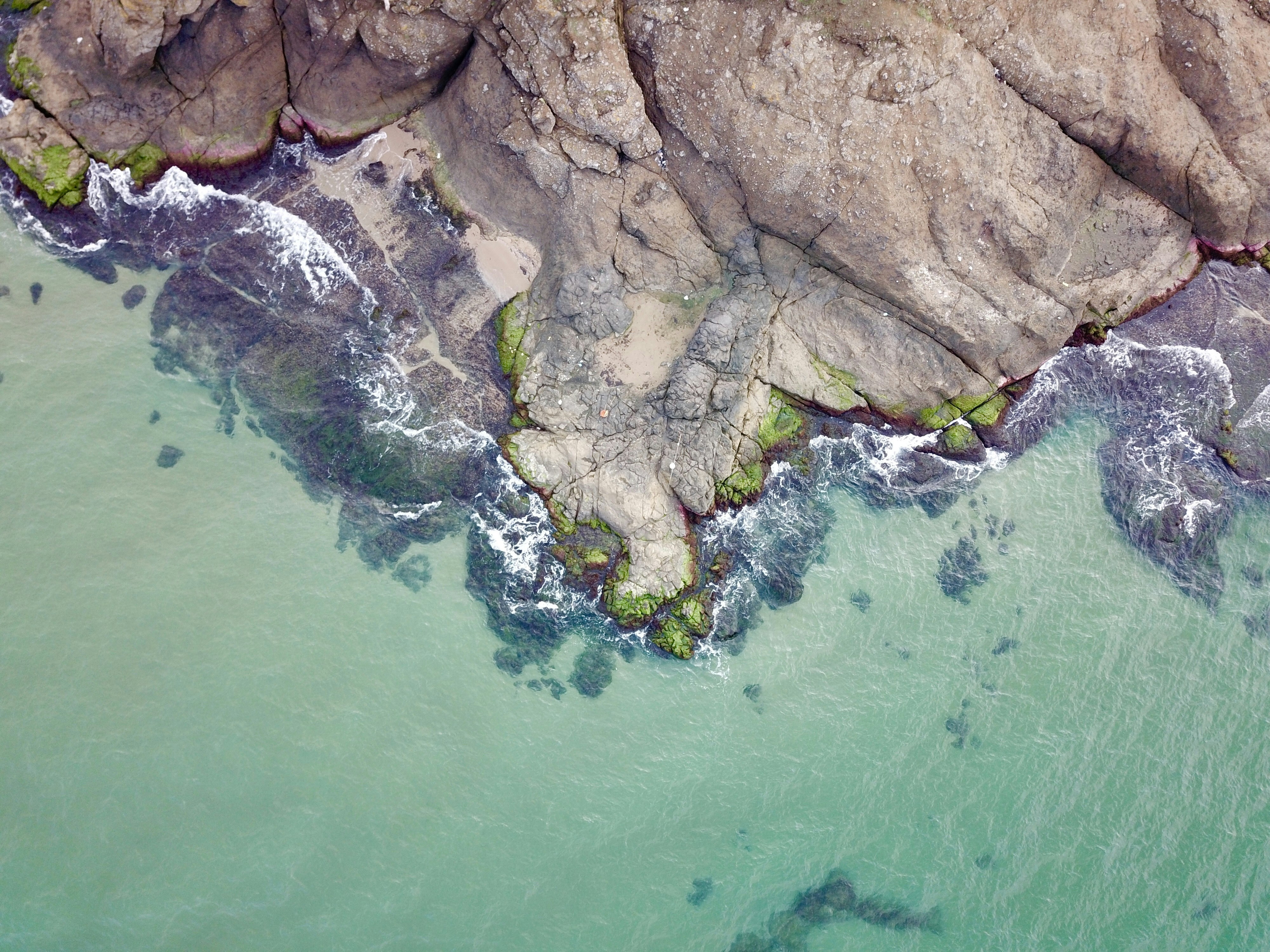 Aerial view of rocky coastline with turquoise waters and scattered seaweed.