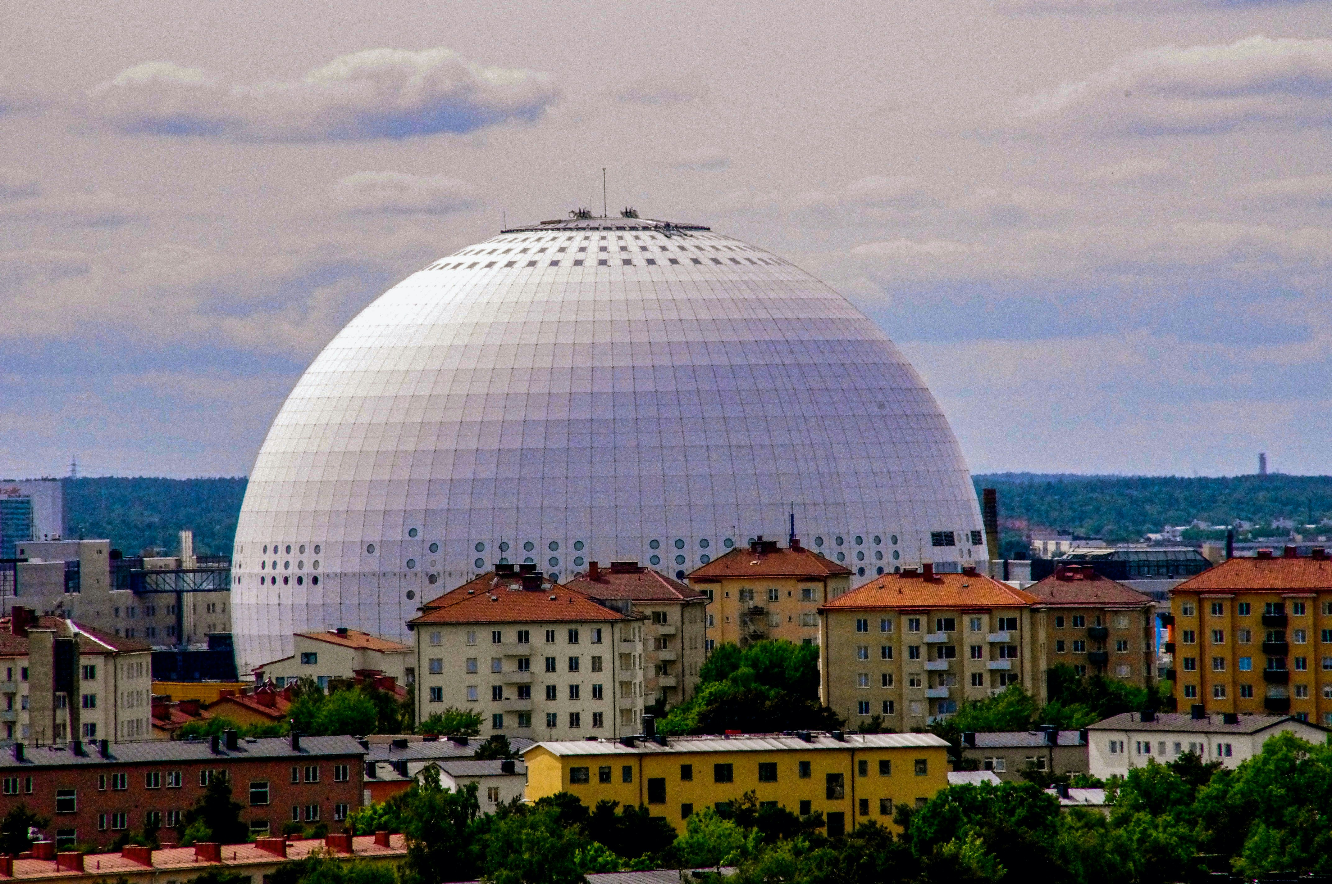 Iconic spherical structure rises above a cityscape, contrasting with surrounding residential buildings. The scene captures a blend of modern architecture and urban life.