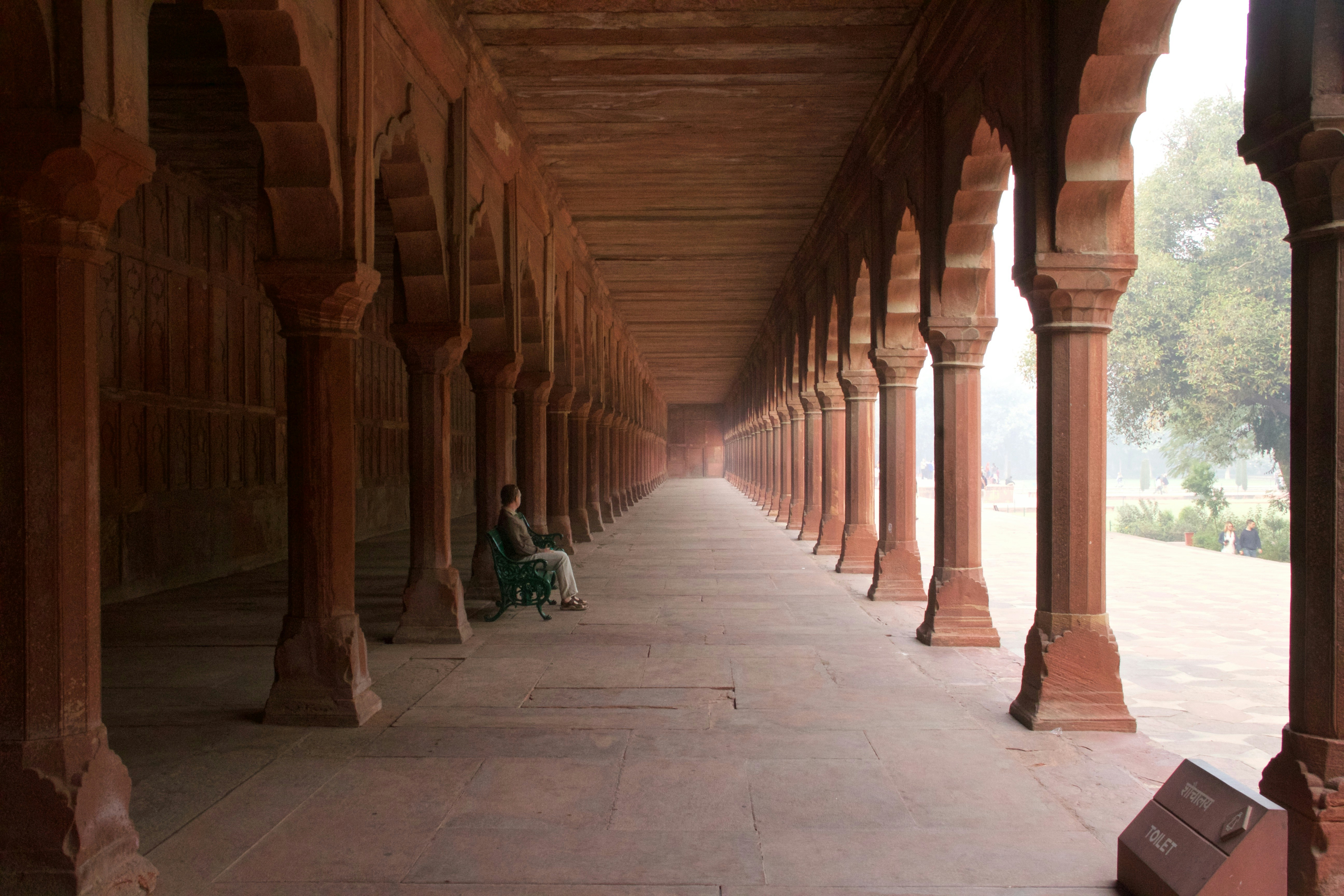Man sitting in a long corridor lined with ornate columns, creating a sense of depth and symmetry.
