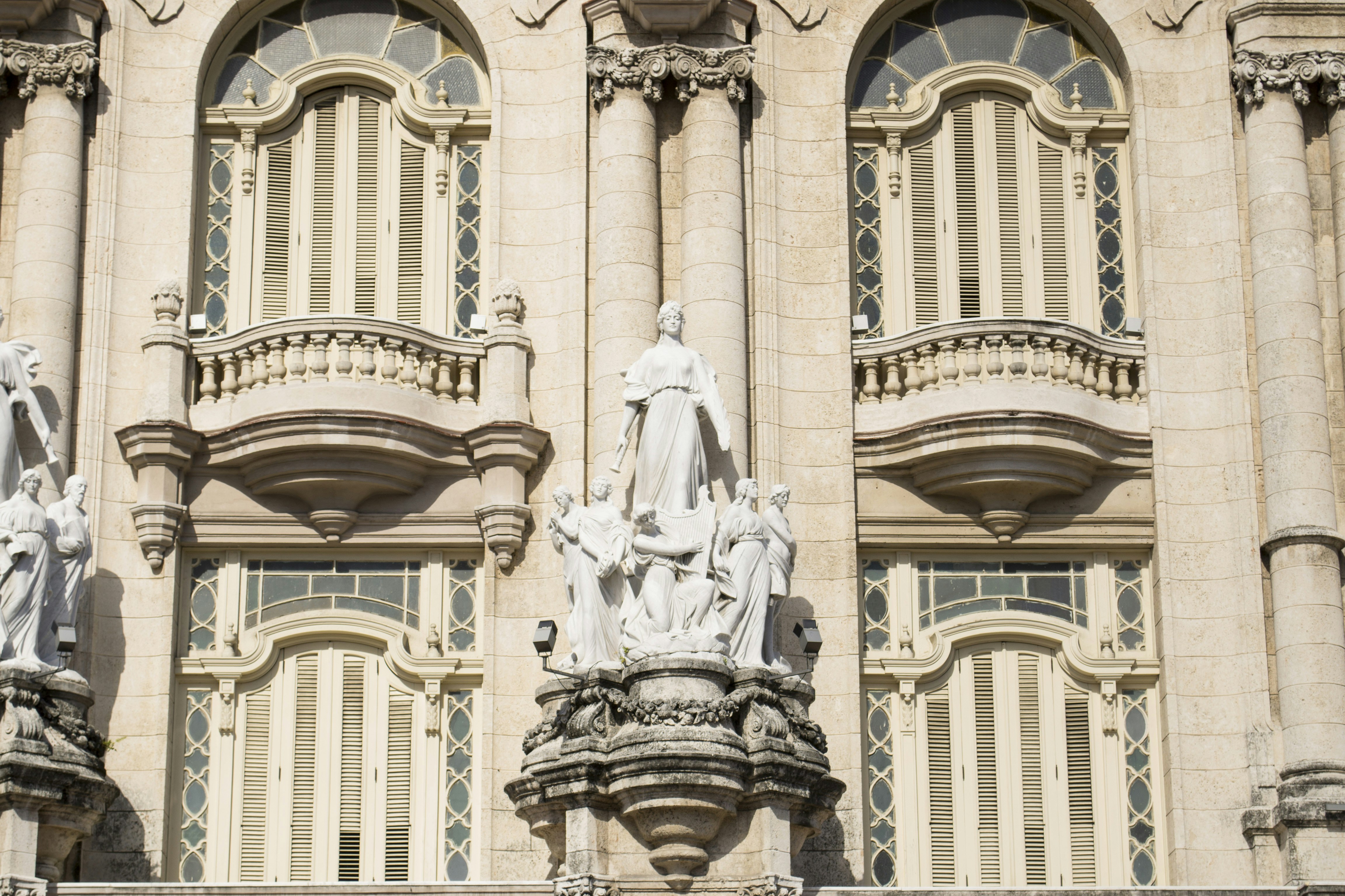 This image captures the grandeur of a historic building's facade, adorned with intricate sculptures and elegant architectural details. The soft beige of the stone contrasts beautifully with the crisp white of the statues, creating a harmonious visual impact. Bathed in natural light, the scene evokes a sense of timeless elegance and artistic mastery.