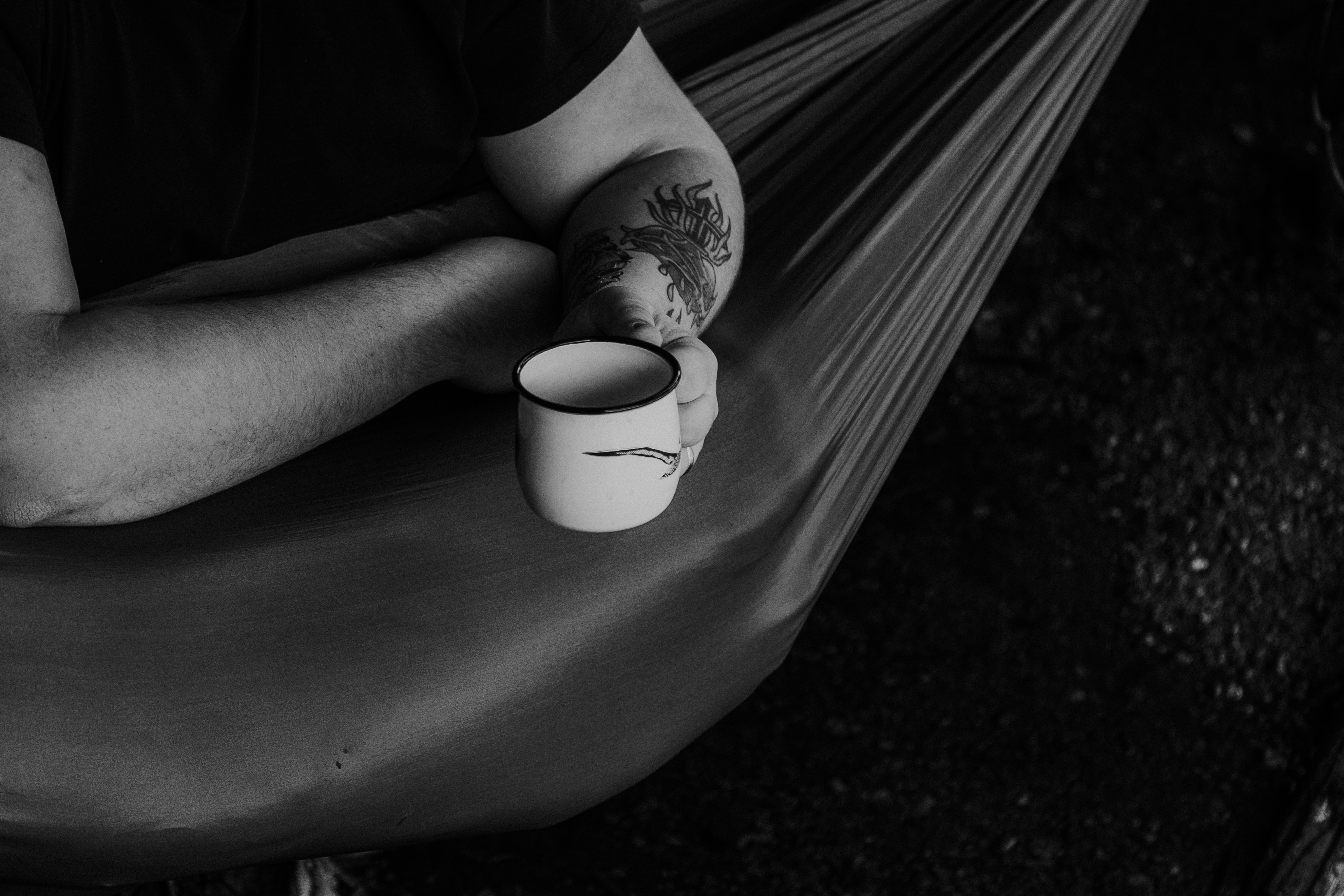 Monochrome Pause: a tattooed arm cradles a white mug in a hammock