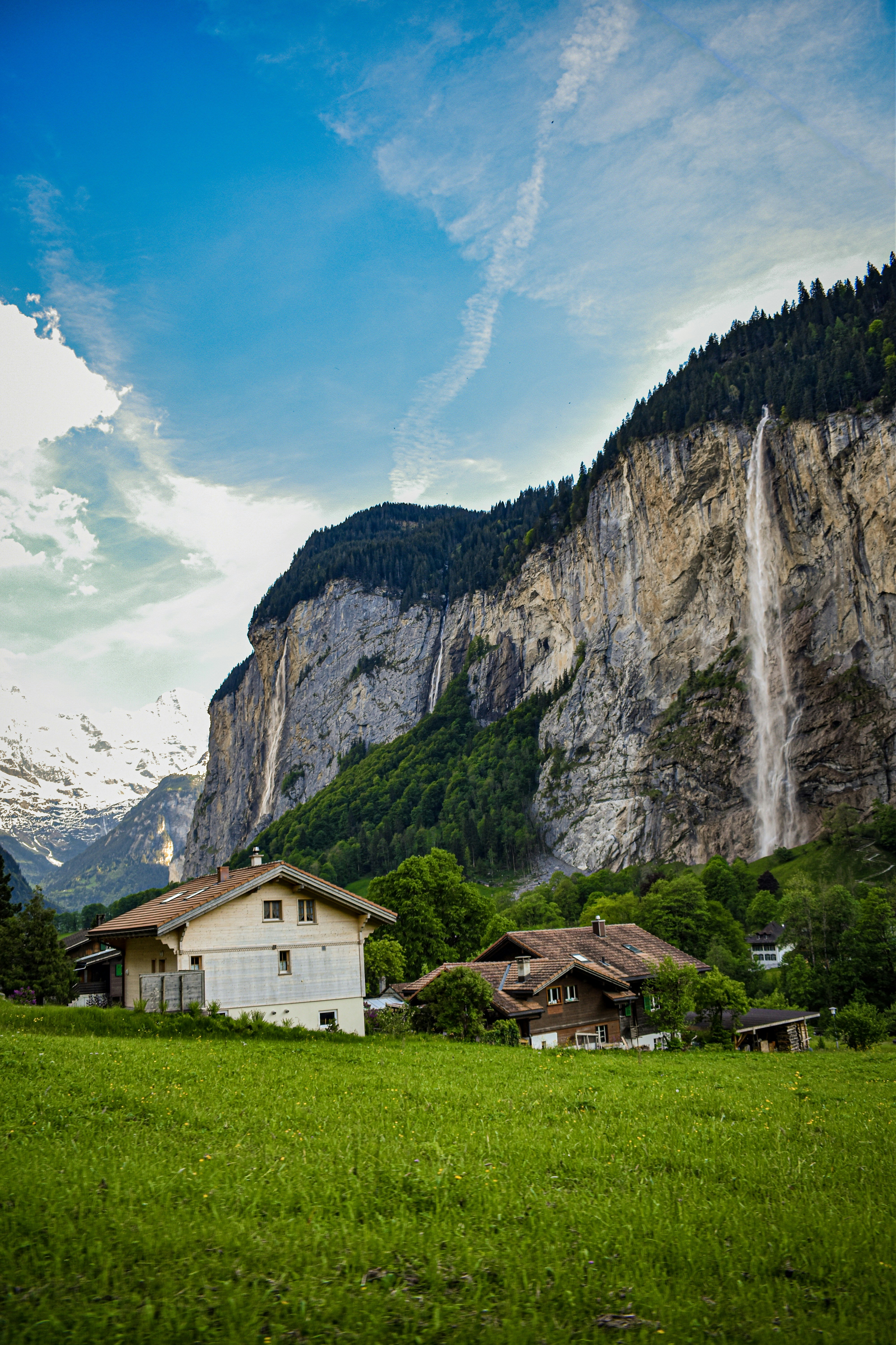 A serene landscape showcasing traditional Swiss chalets nestled in lush greenery, with a majestic waterfall cascading down the rocky cliffs in the background.