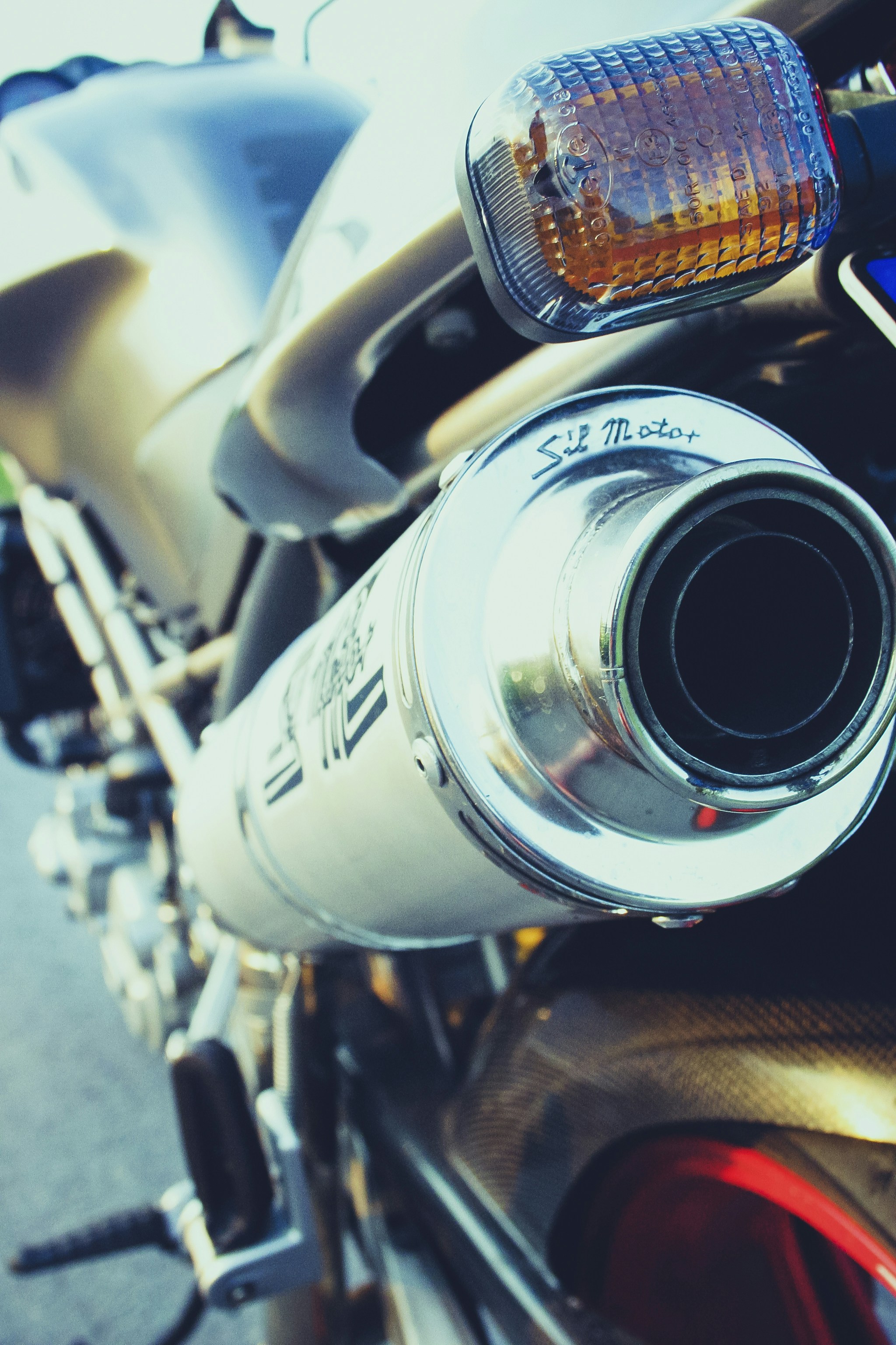 Close-up of a motorcycle's chrome exhaust pipe and rear light assembly, highlighting sleek design and engineering.