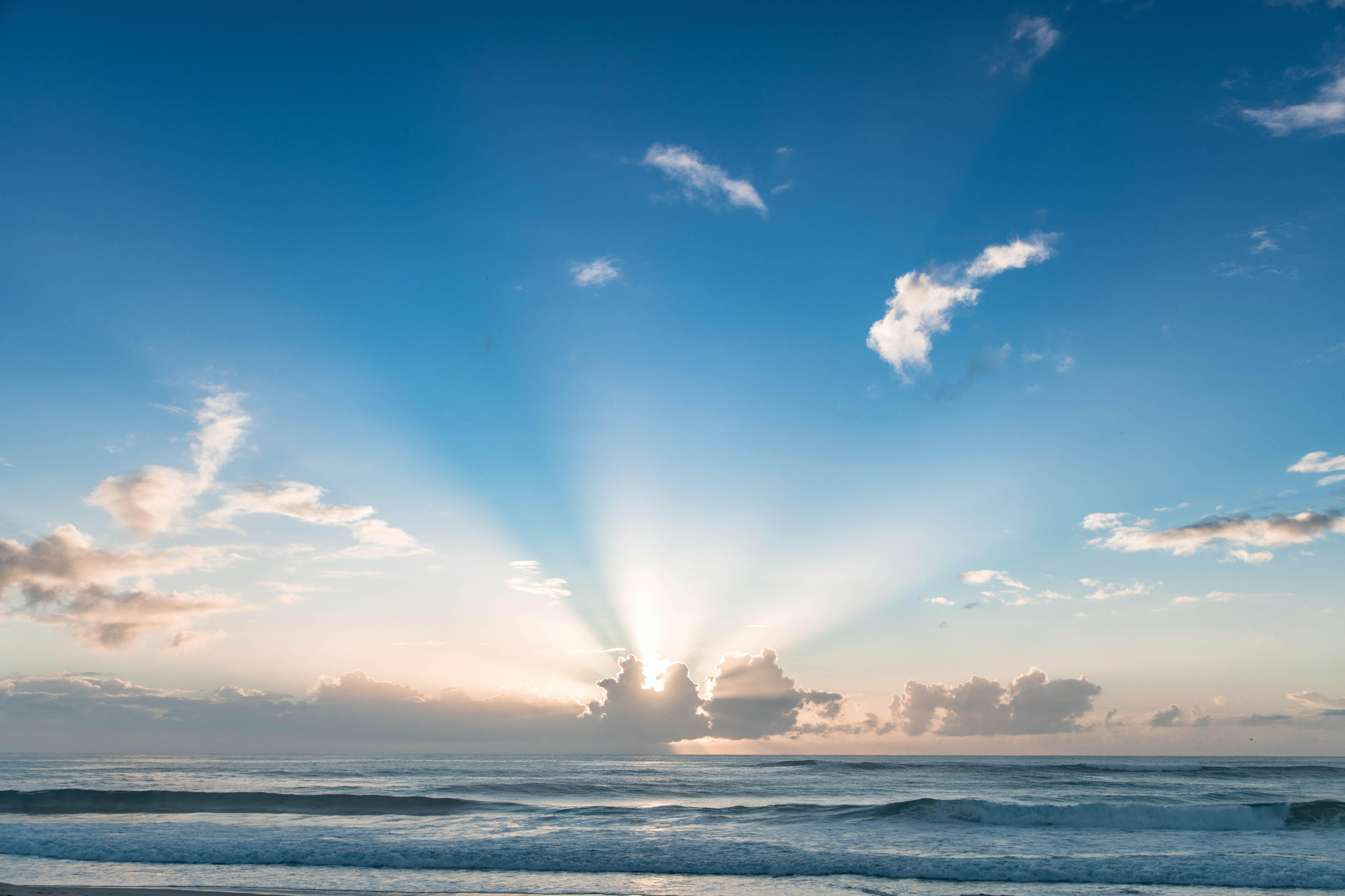 Dramatic seascape at sunrise with sun rays bursting from behind clouds over a calm horizon; expansive sky and layered waves add depth. (photographic still) 