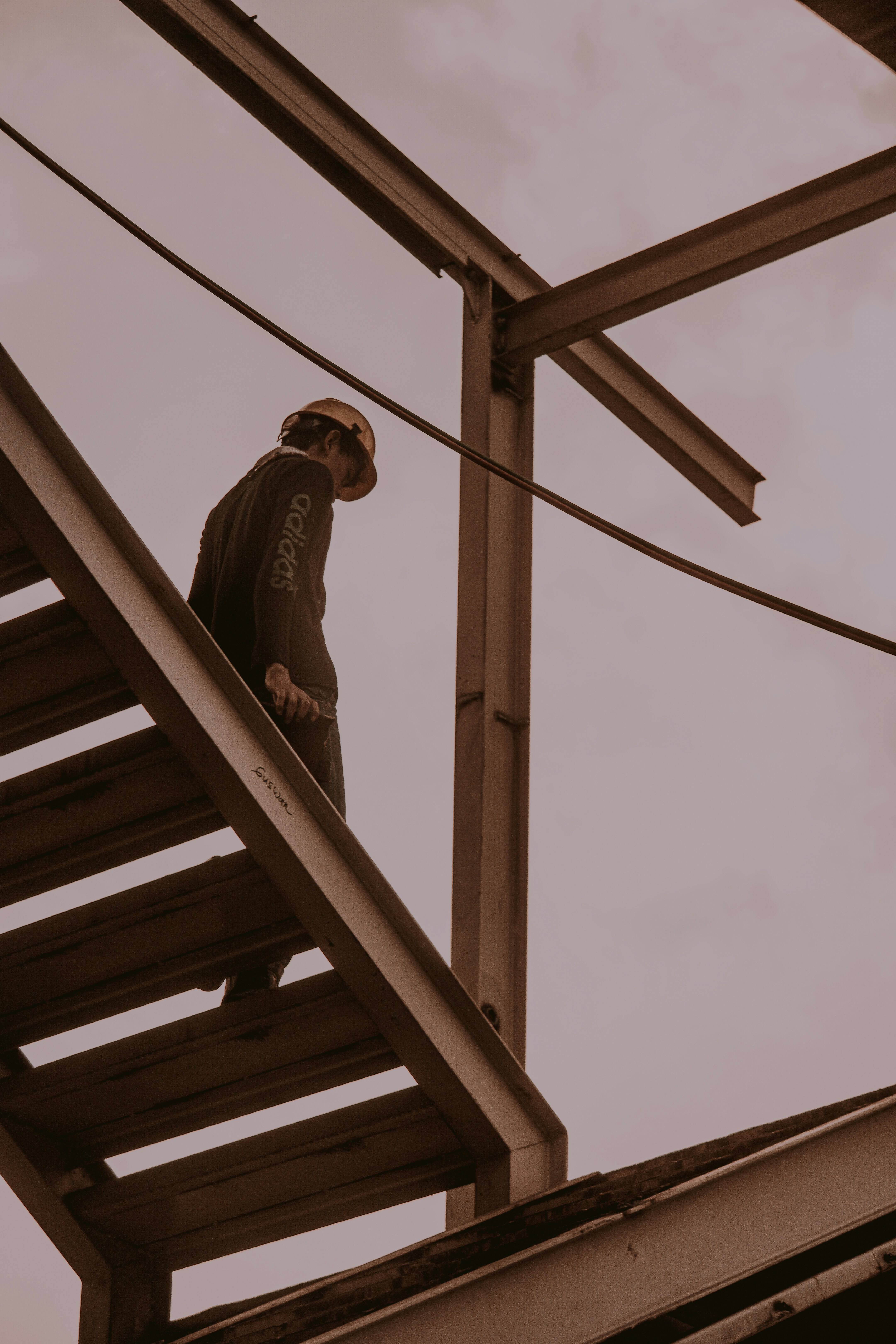 A figure navigating a metallic staircase, surrounded by industrial architecture, evoking a sense of exploration. The sepia tone adds a nostalgic atmosphere.