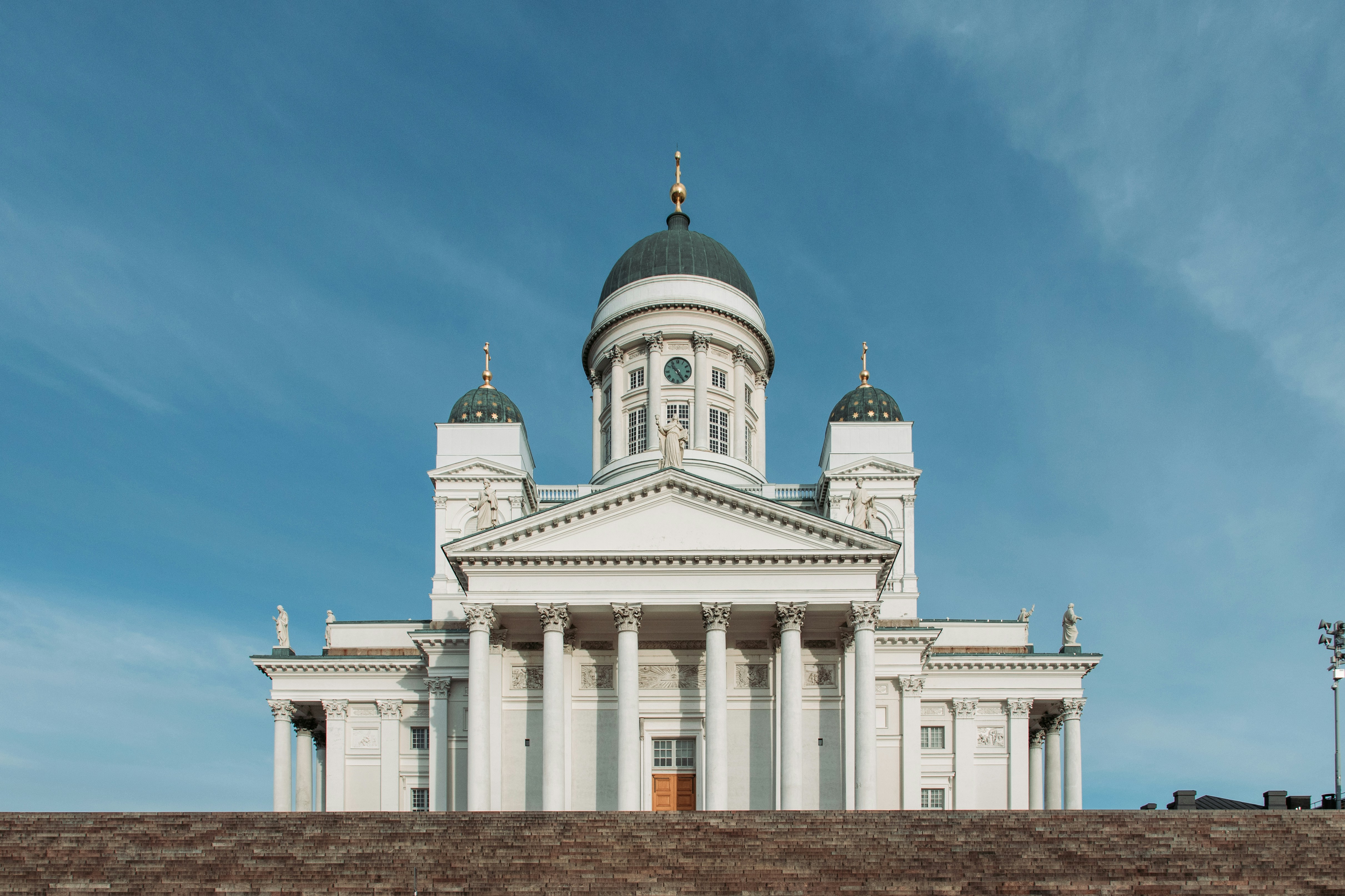 Grand neoclassical cathedral with a central dome and two smaller towers against a clear blue sky.
