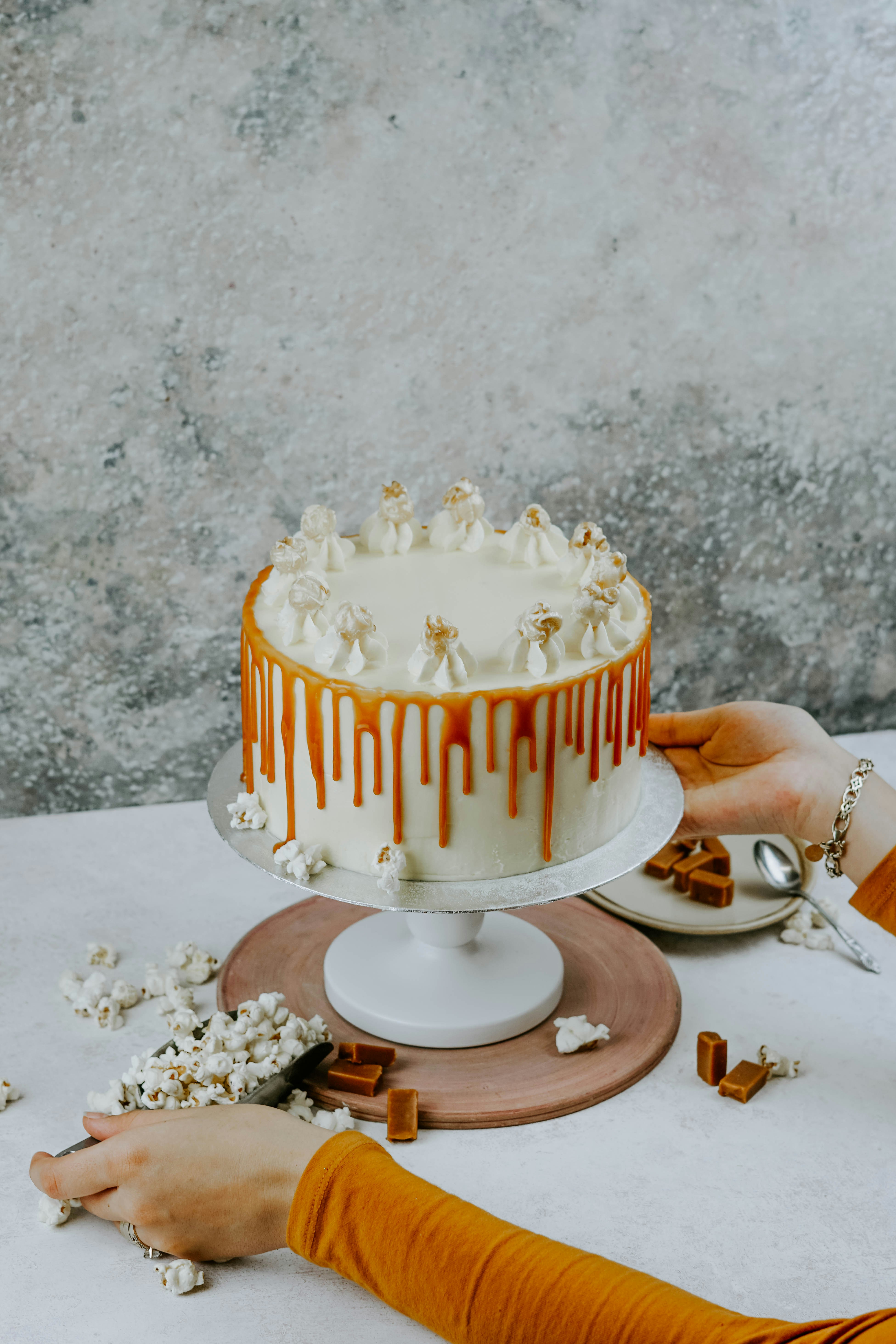 A beautifully decorated cake with caramel drips and popcorn accents, set against a textured background. The scene captures a moment of indulgence and creativity.