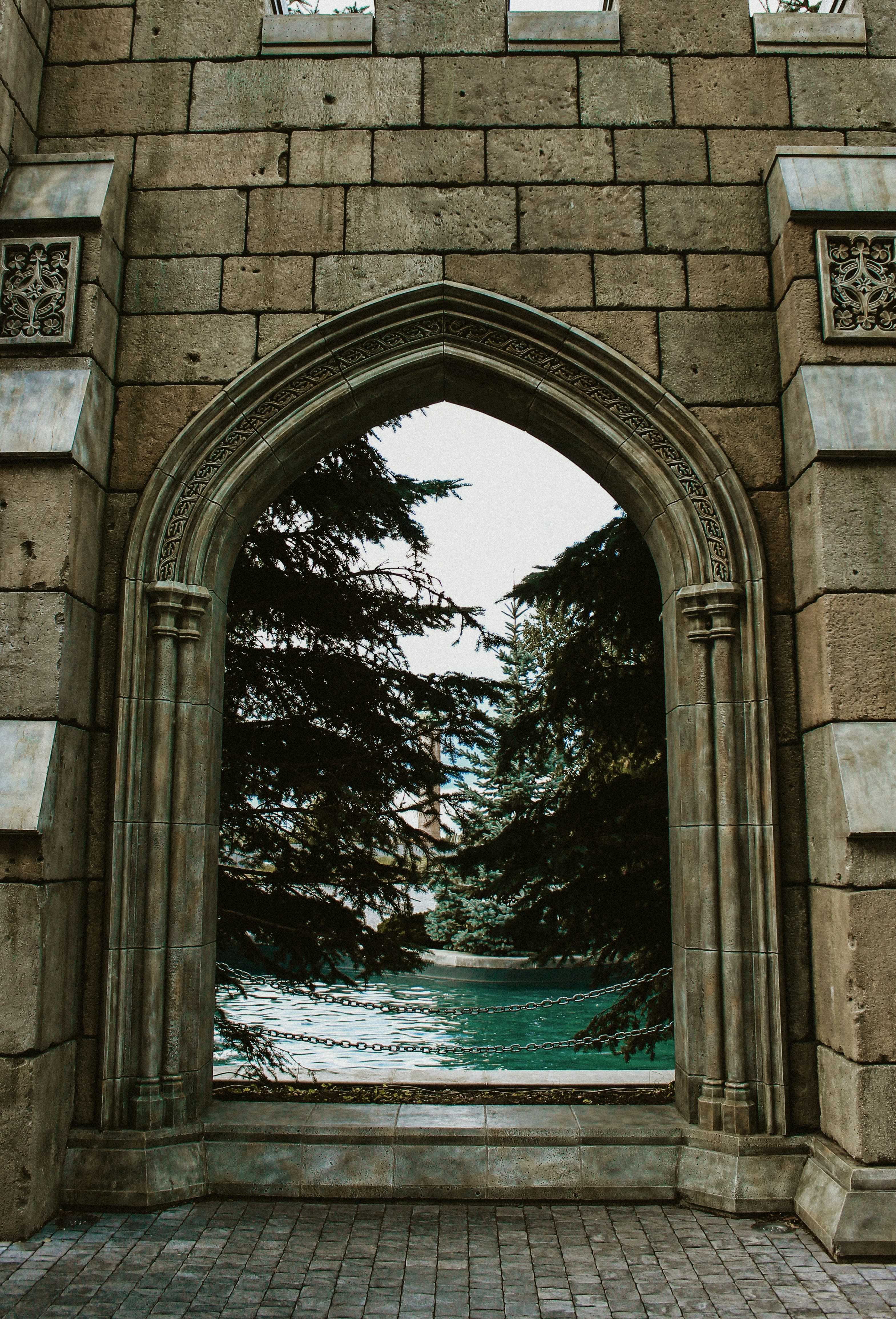 Intricate stone archway frames a tranquil view of lush greenery and a serene body of water beyond.