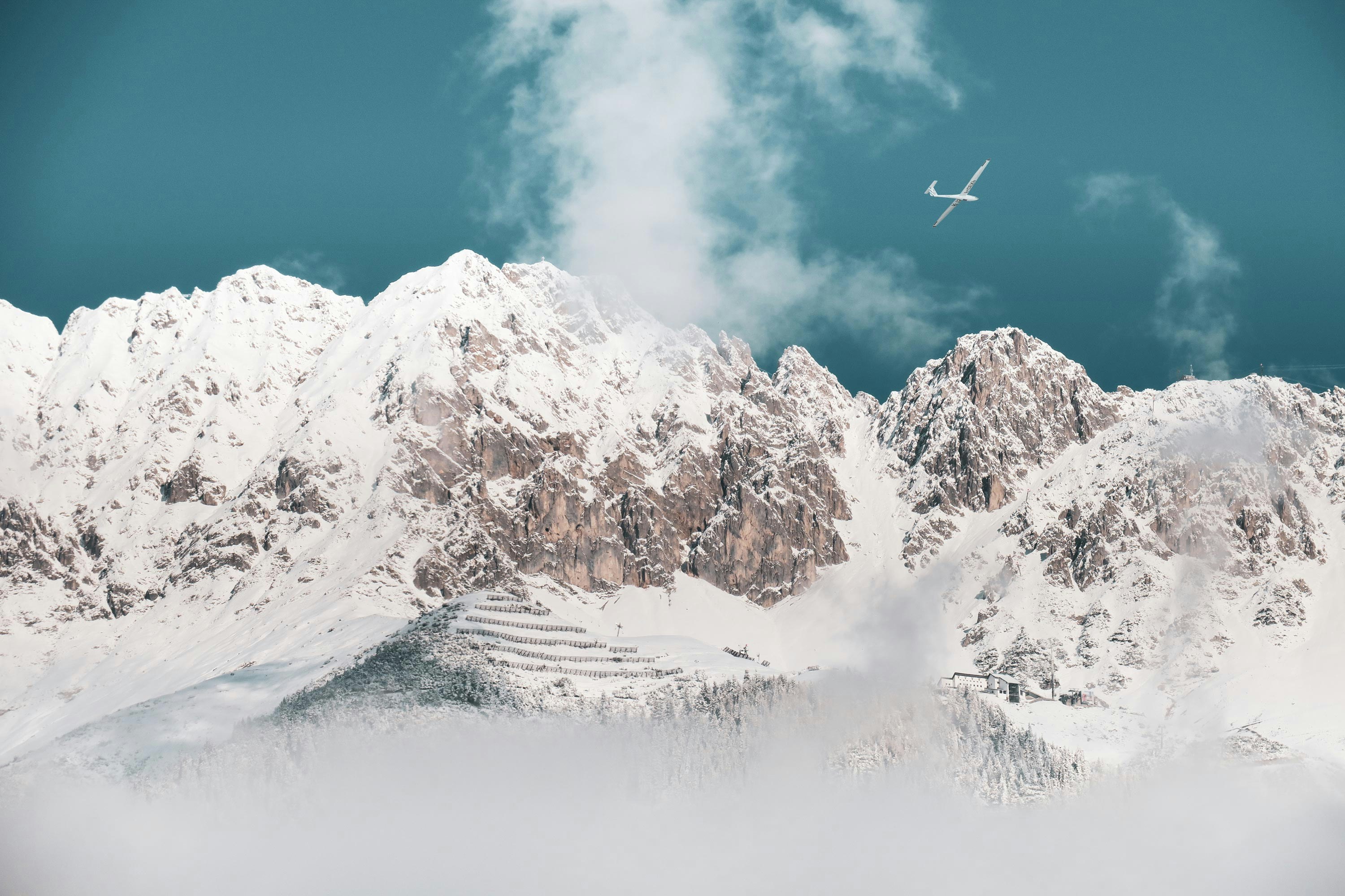 Snow-covered mountain range under a clear blue sky with a small plane flying overhead.