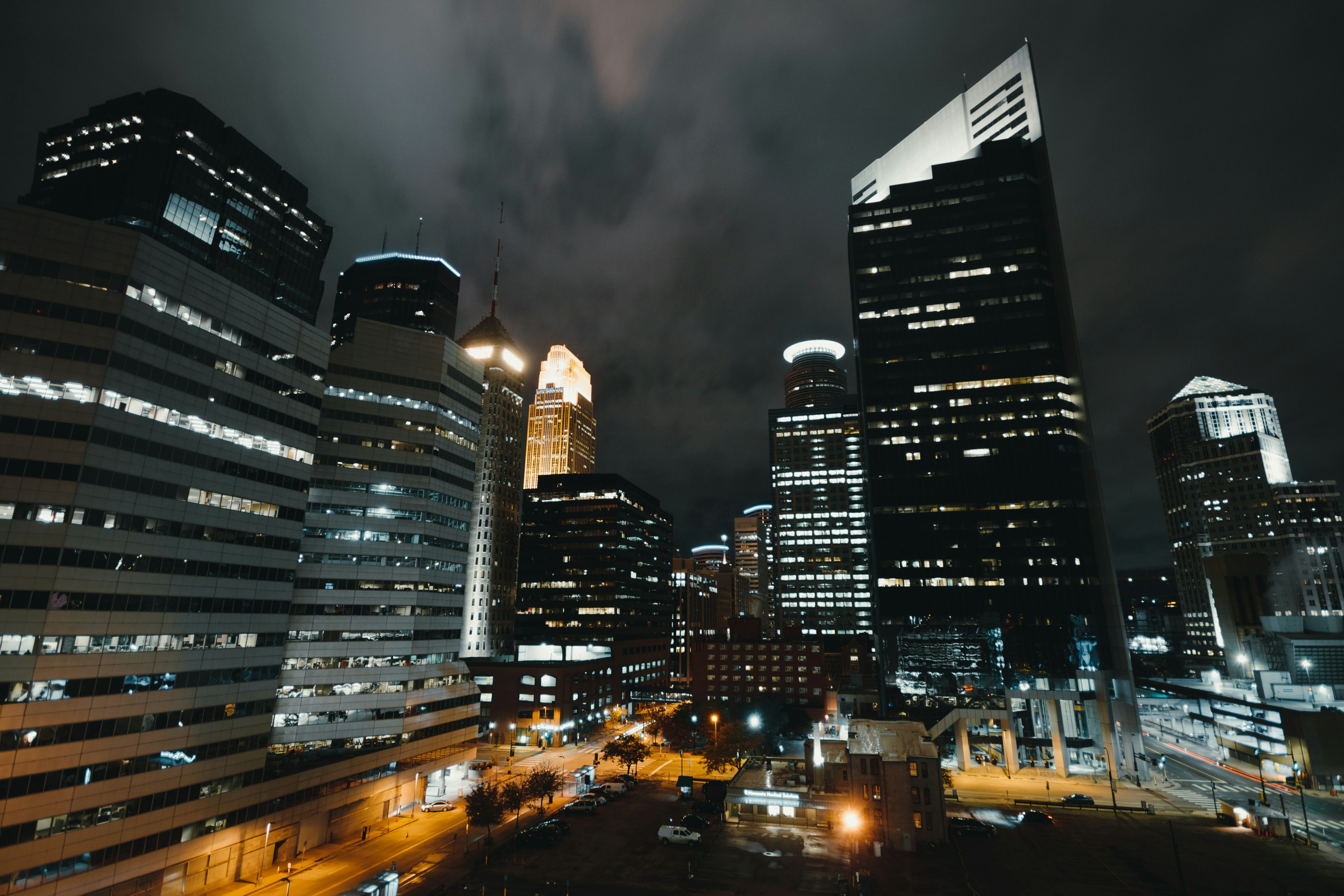 Illuminated high-rise buildings dominate the cityscape under a cloudy night sky.