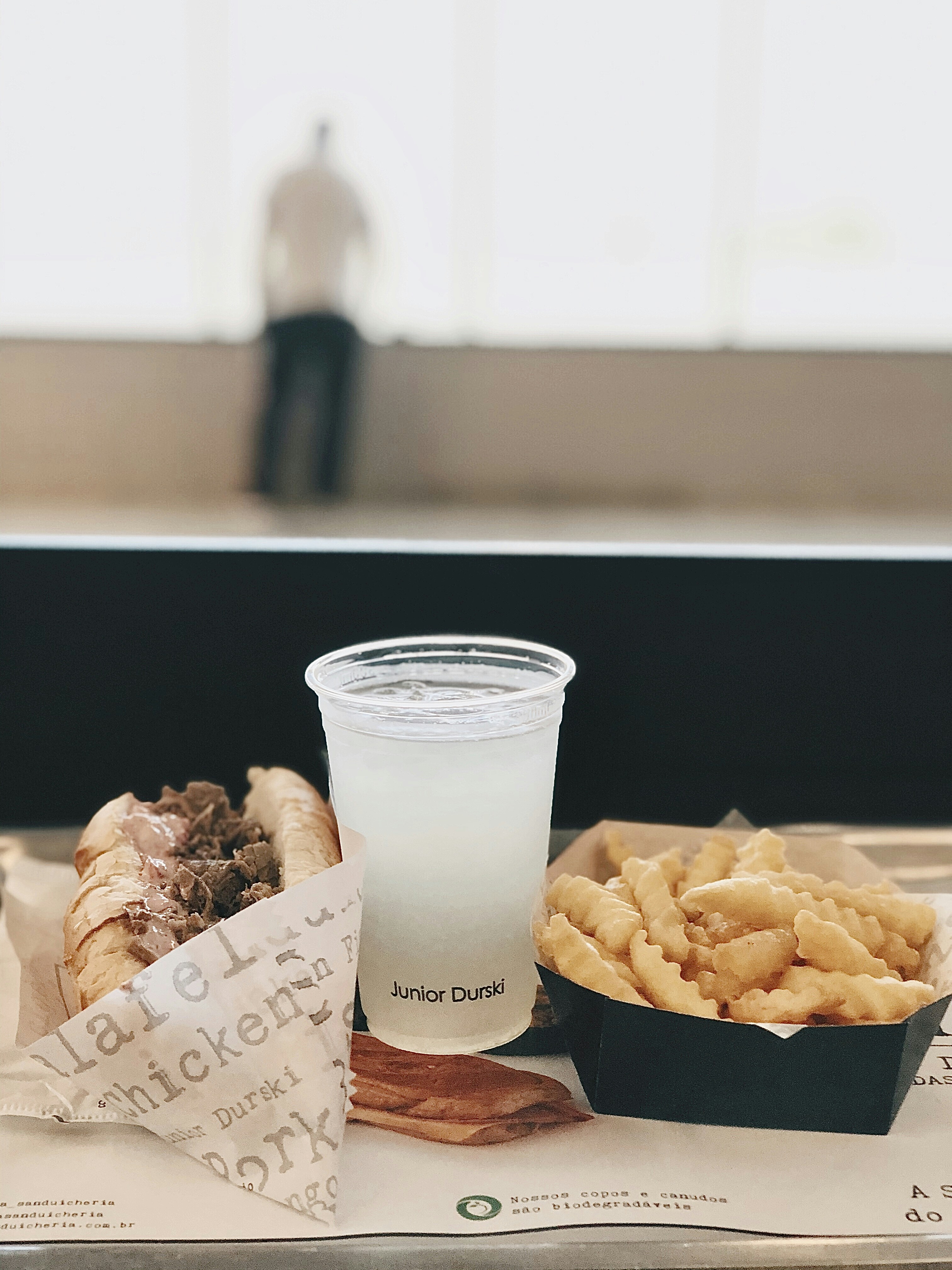A delicious spread featuring a sandwich filled with savory meat, a refreshing drink in a clear cup, and a side of crinkle-cut fries.