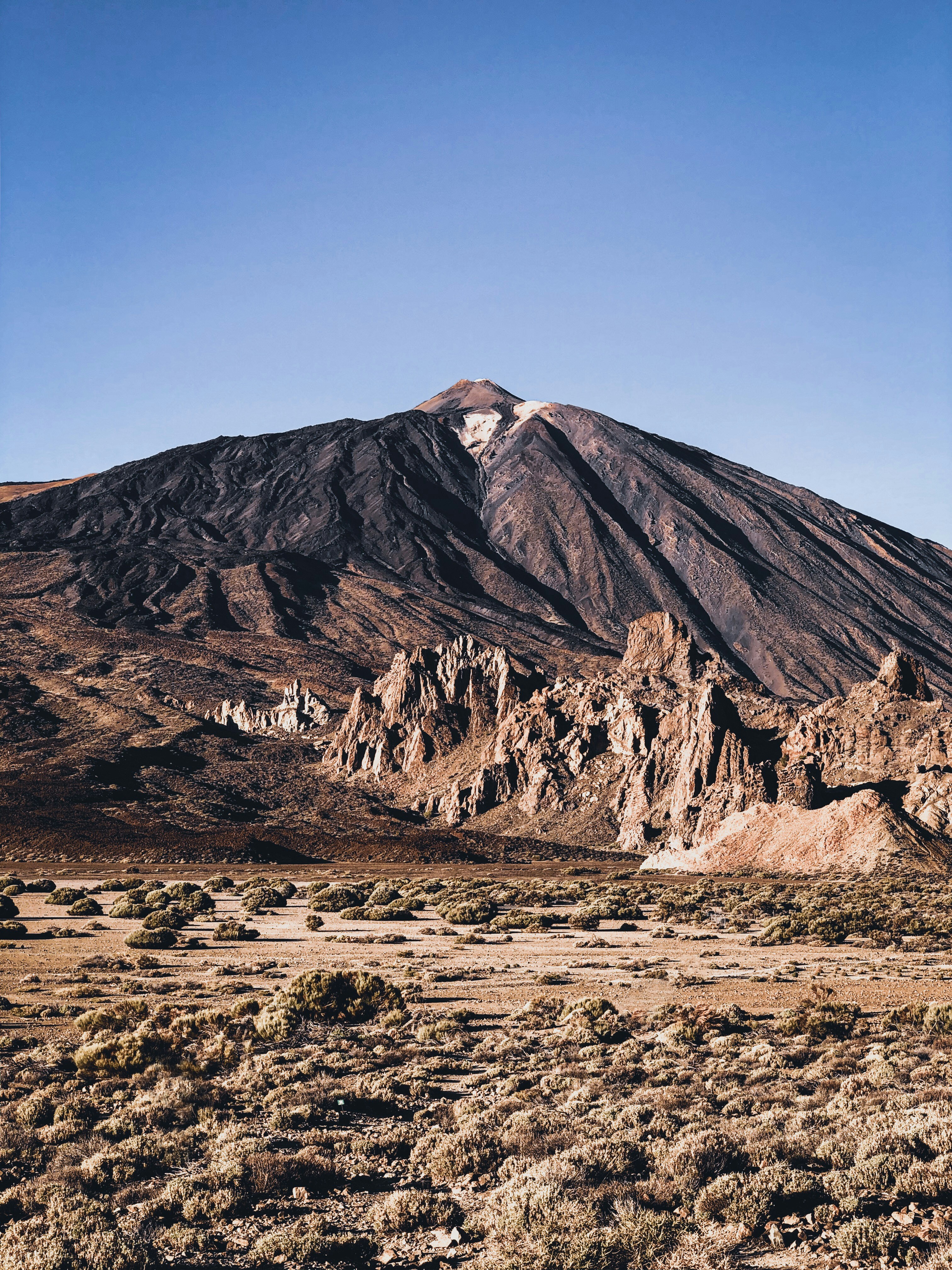 Majestic mountain rising above rugged terrain, showcasing unique geological formations and sparse vegetation under a clear blue sky.
