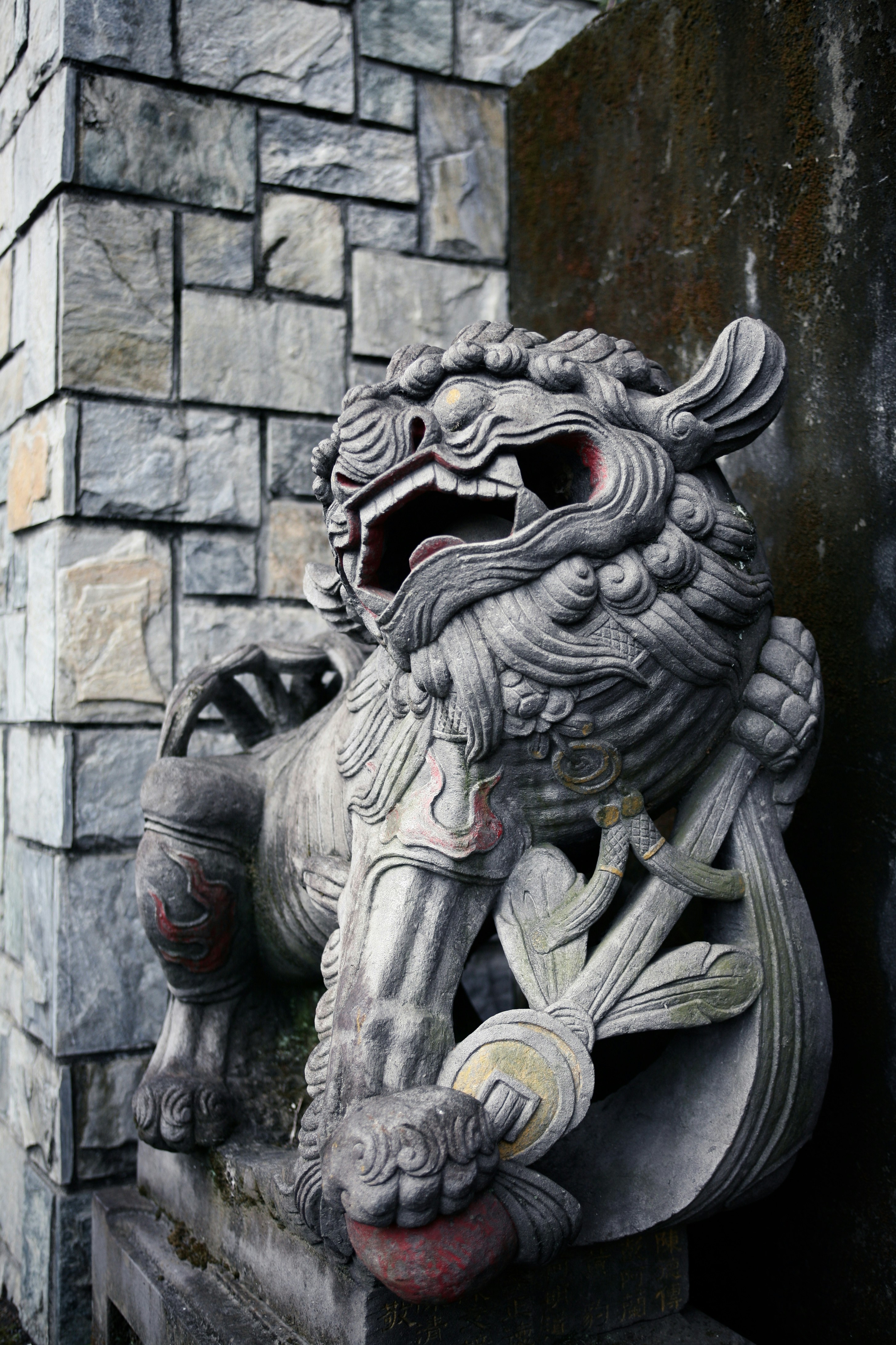 Intricately carved stone lion sculpture positioned against a textured stone wall, showcasing its fierce expression and detailed craftsmanship.