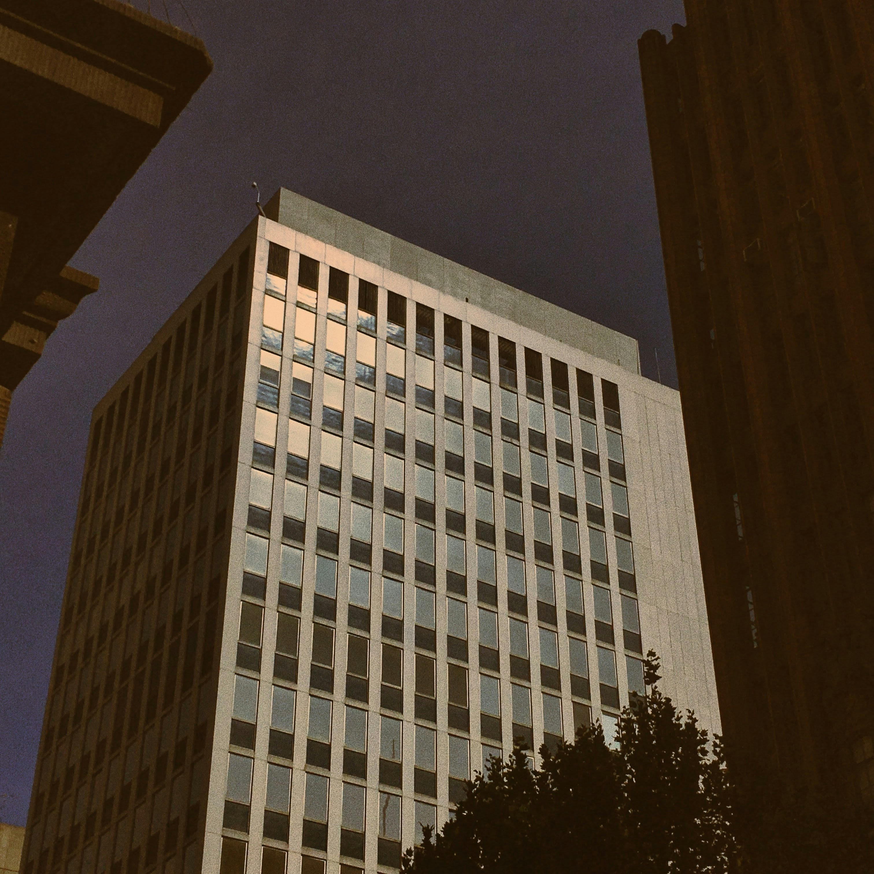 A tall office building reflecting the evening sky, framed by nearby structures. The architectural lines create a striking contrast against the backdrop.