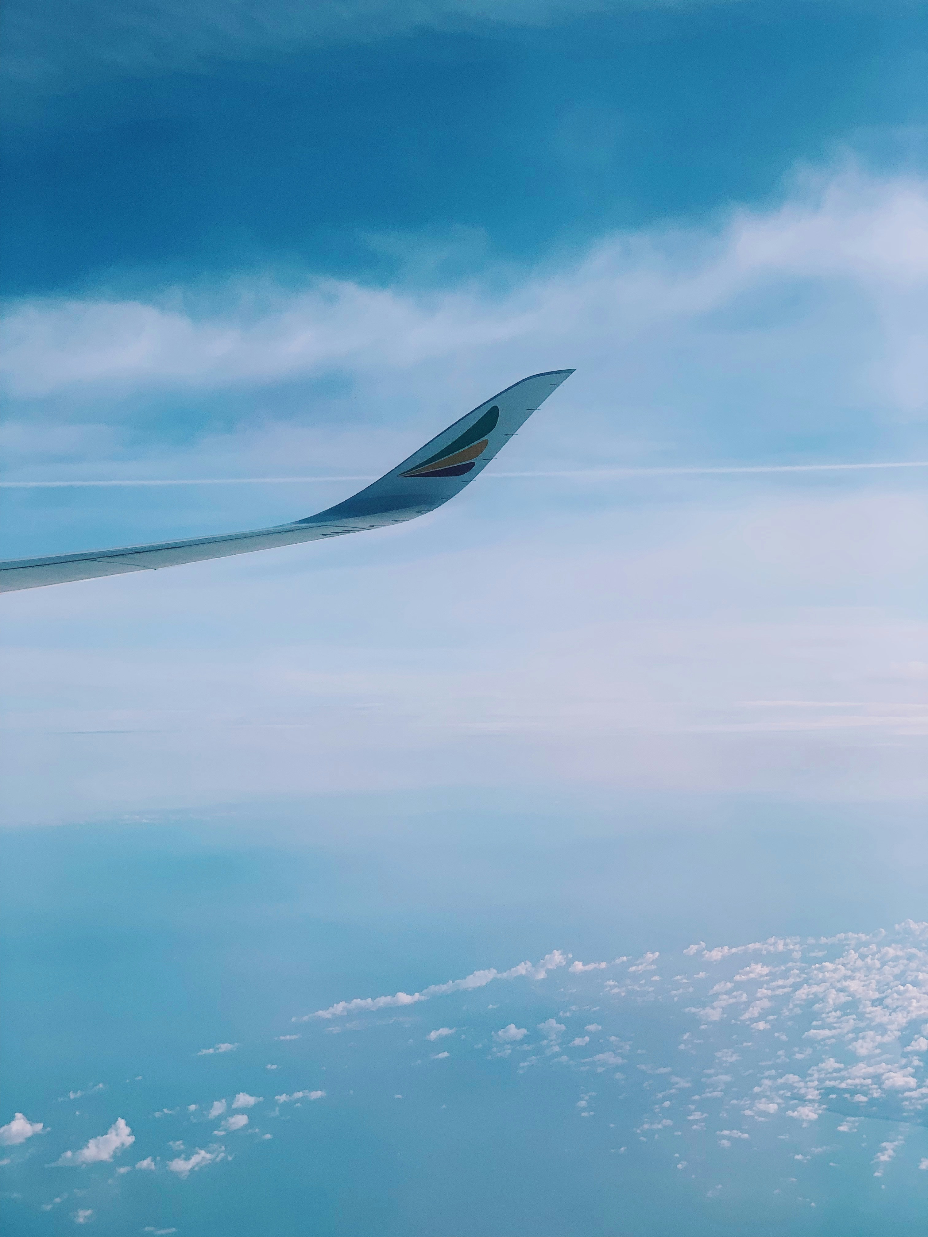 Airplane wing gliding through a serene blue sky, with wispy clouds below.