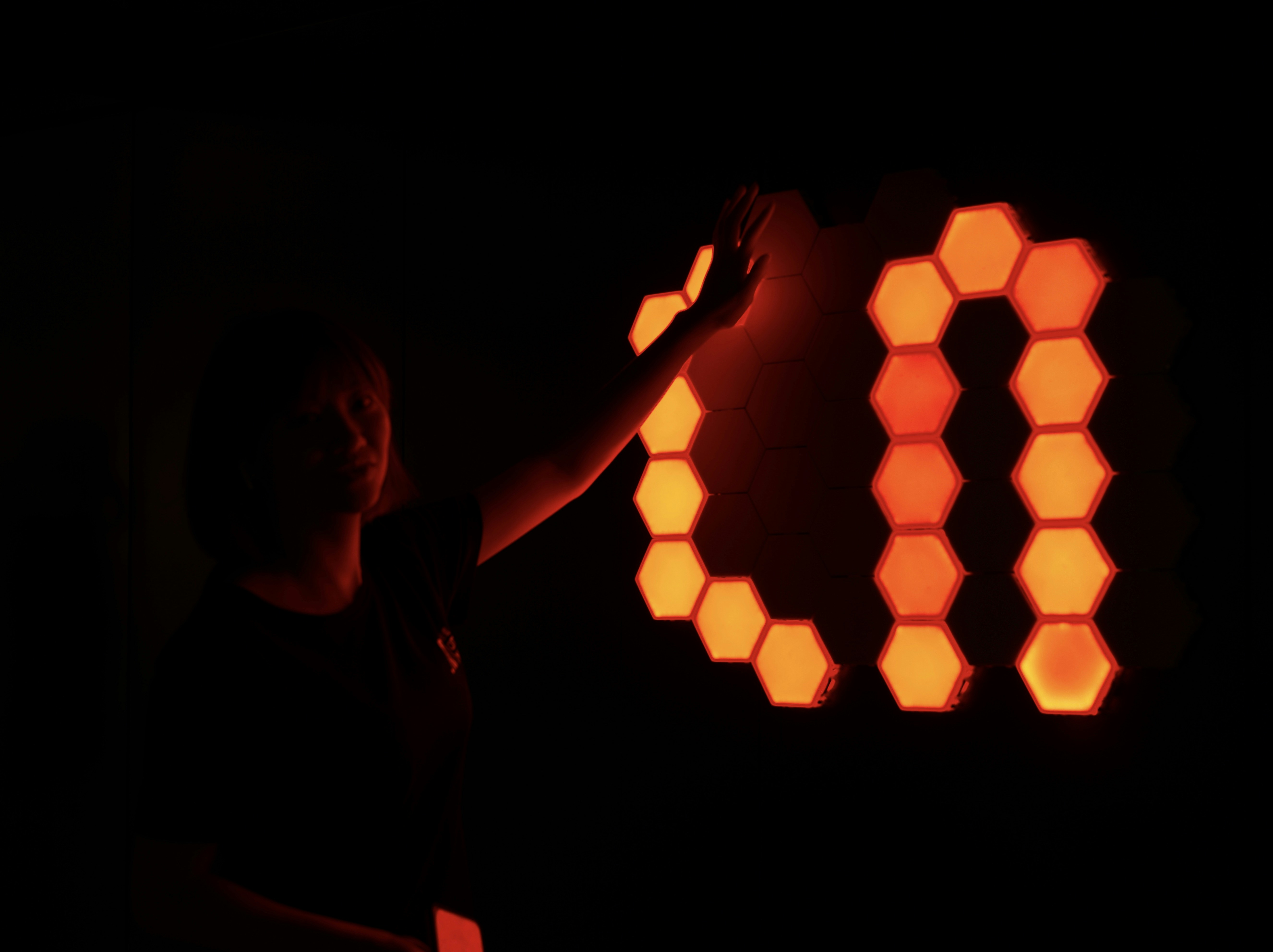 Low‑Light Neon Portrait: Hand Reaches Toward a Hexagonal Light Canvas