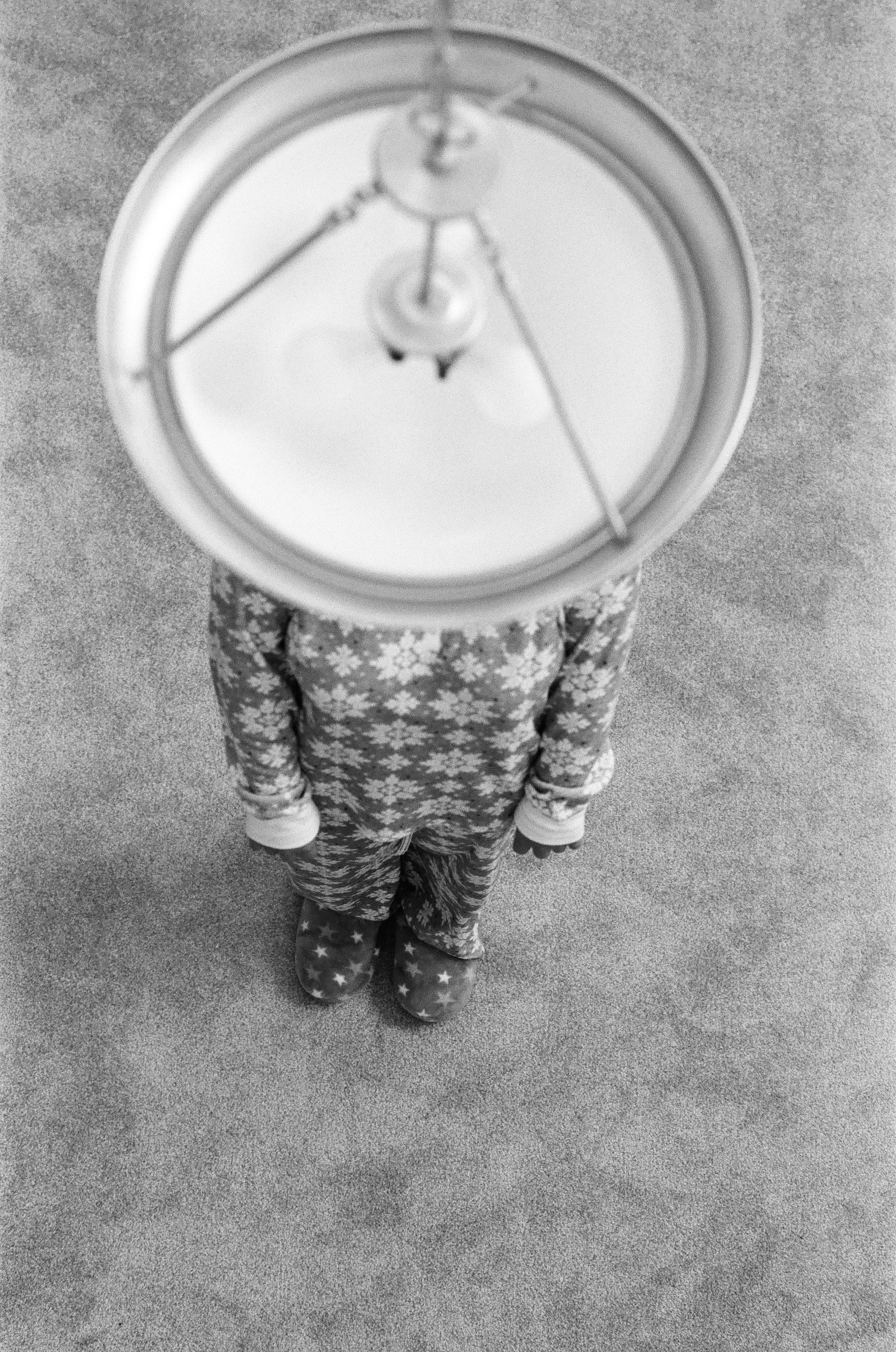 Child standing on soft carpet, partially obscured by a hanging light fixture. The monochrome tones enhance the serene atmosphere.
