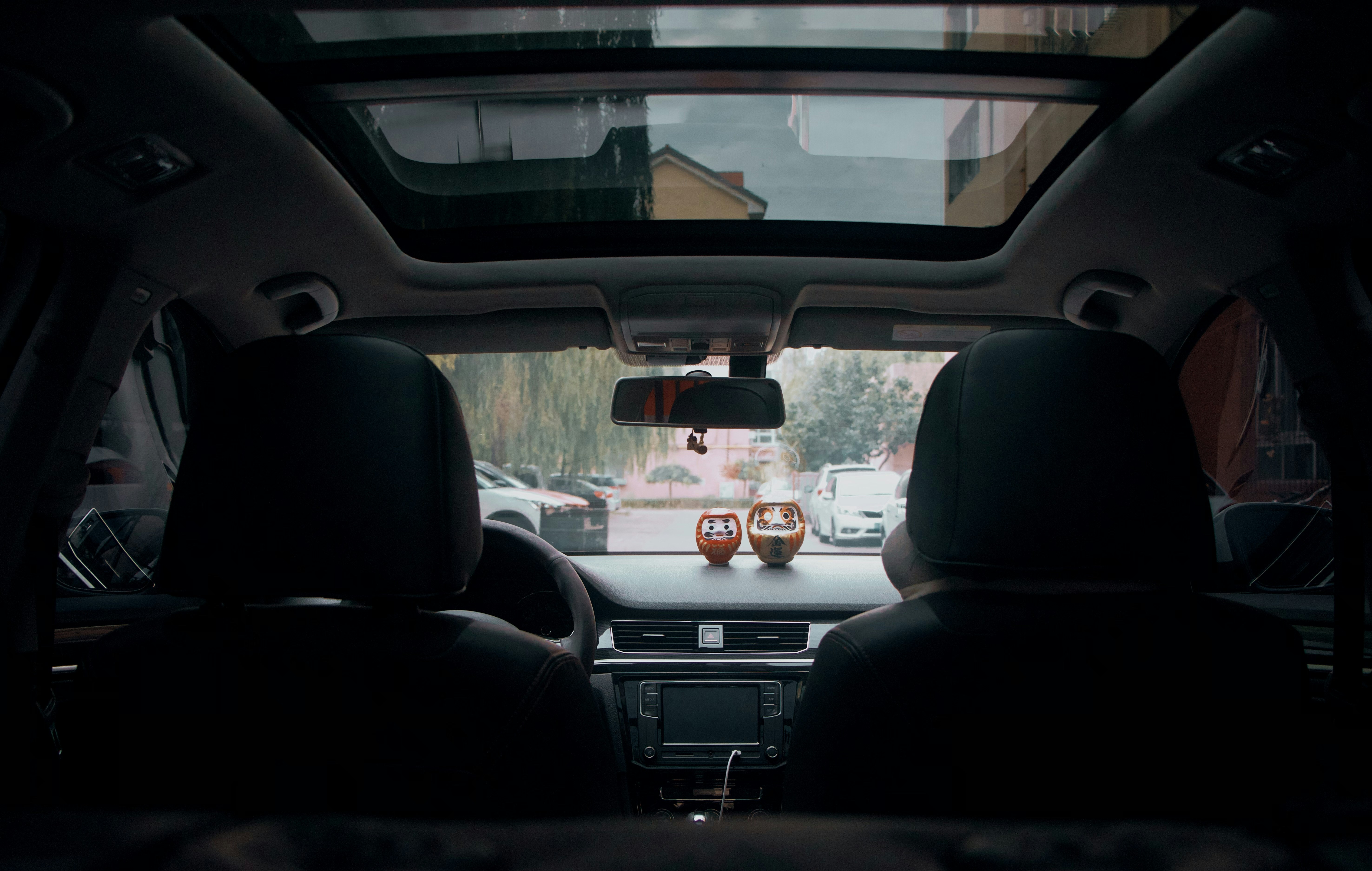 Interior view of a car showcasing the dashboard and sunroof, with decorative items on the dashboard. A glimpse of the outside world through the glass roof.