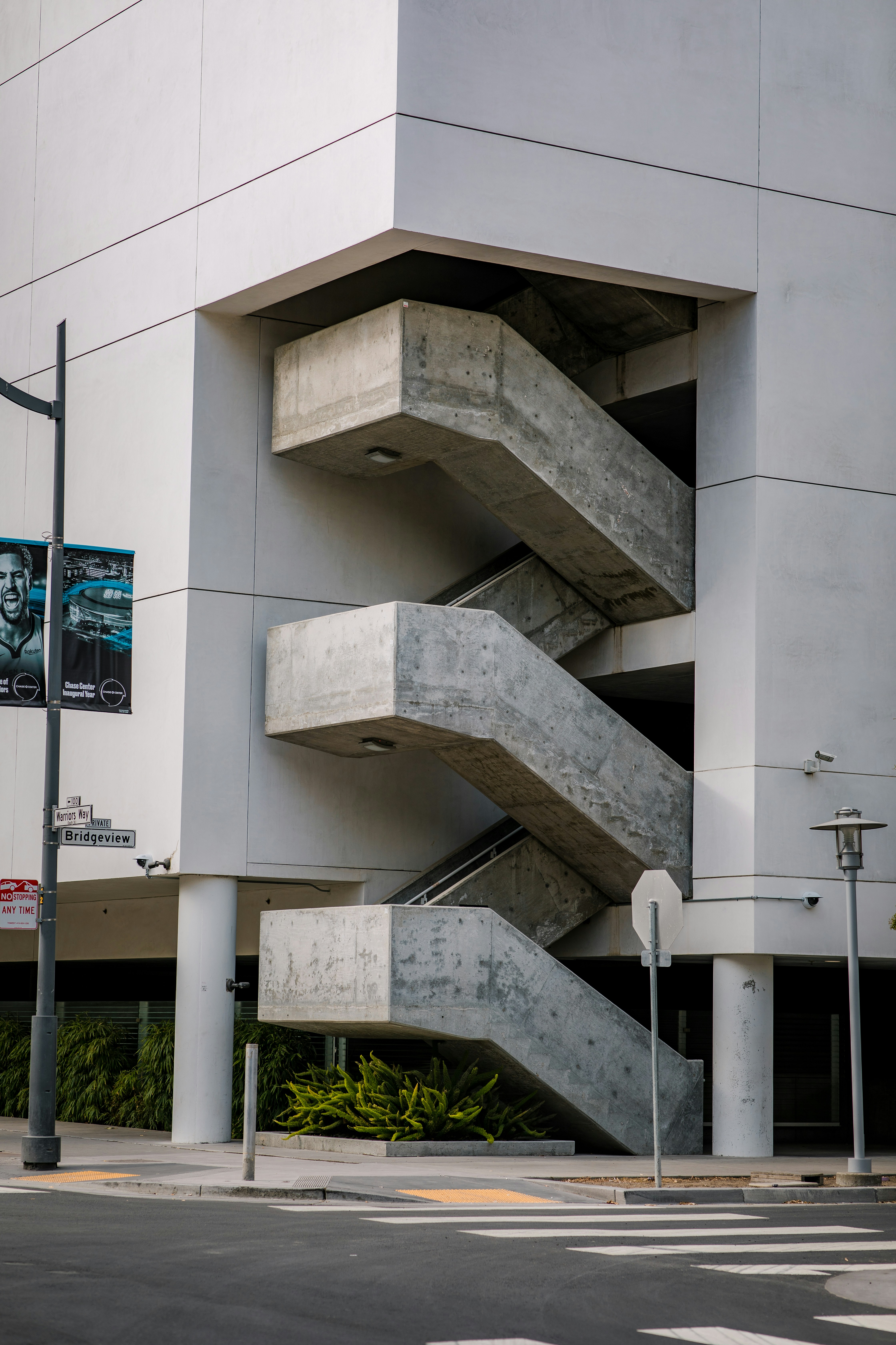 Concrete staircase spiraling around a modern building, framed by urban greenery and street signage.