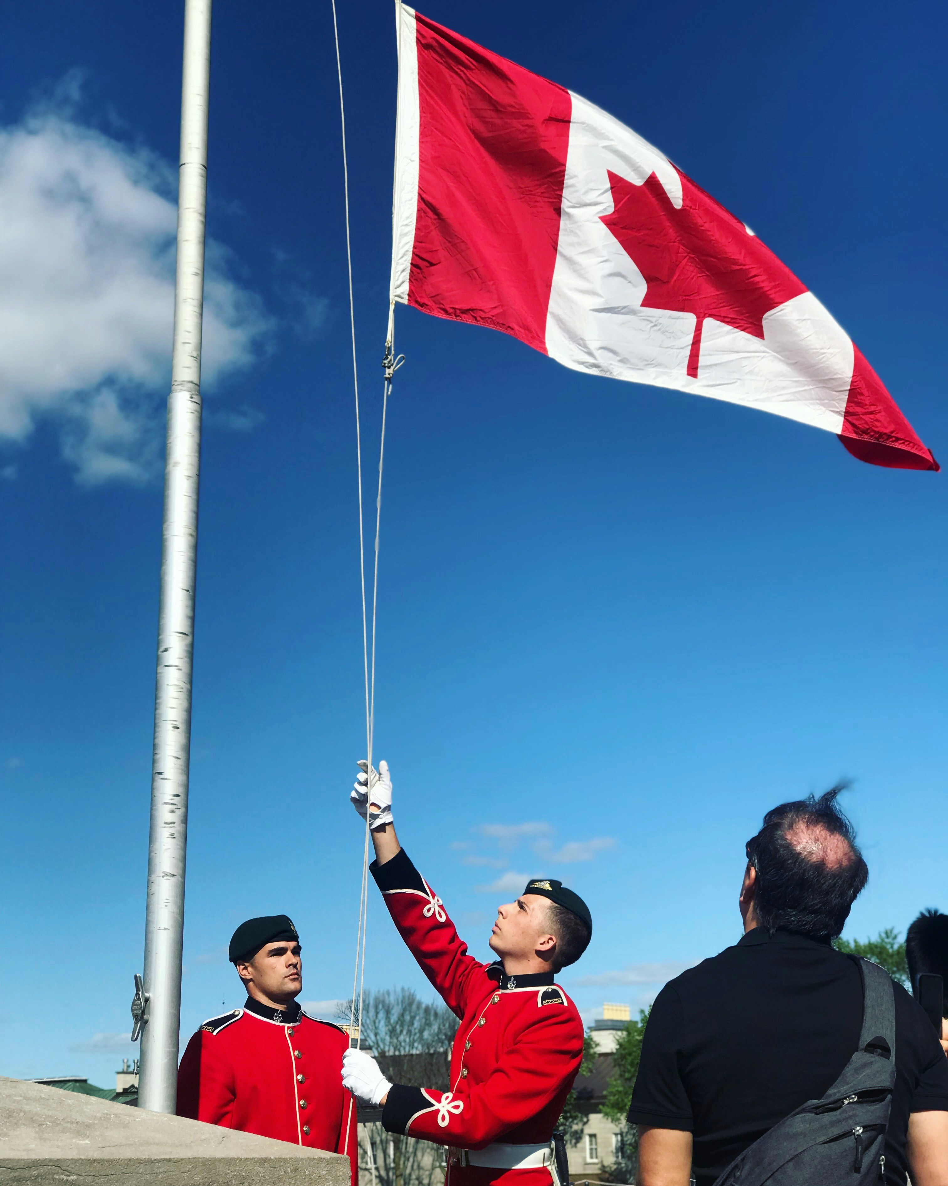 Two soldiers in ceremonial attire hoist the Canadian flag against a clear blue sky, embodying national pride and tradition.