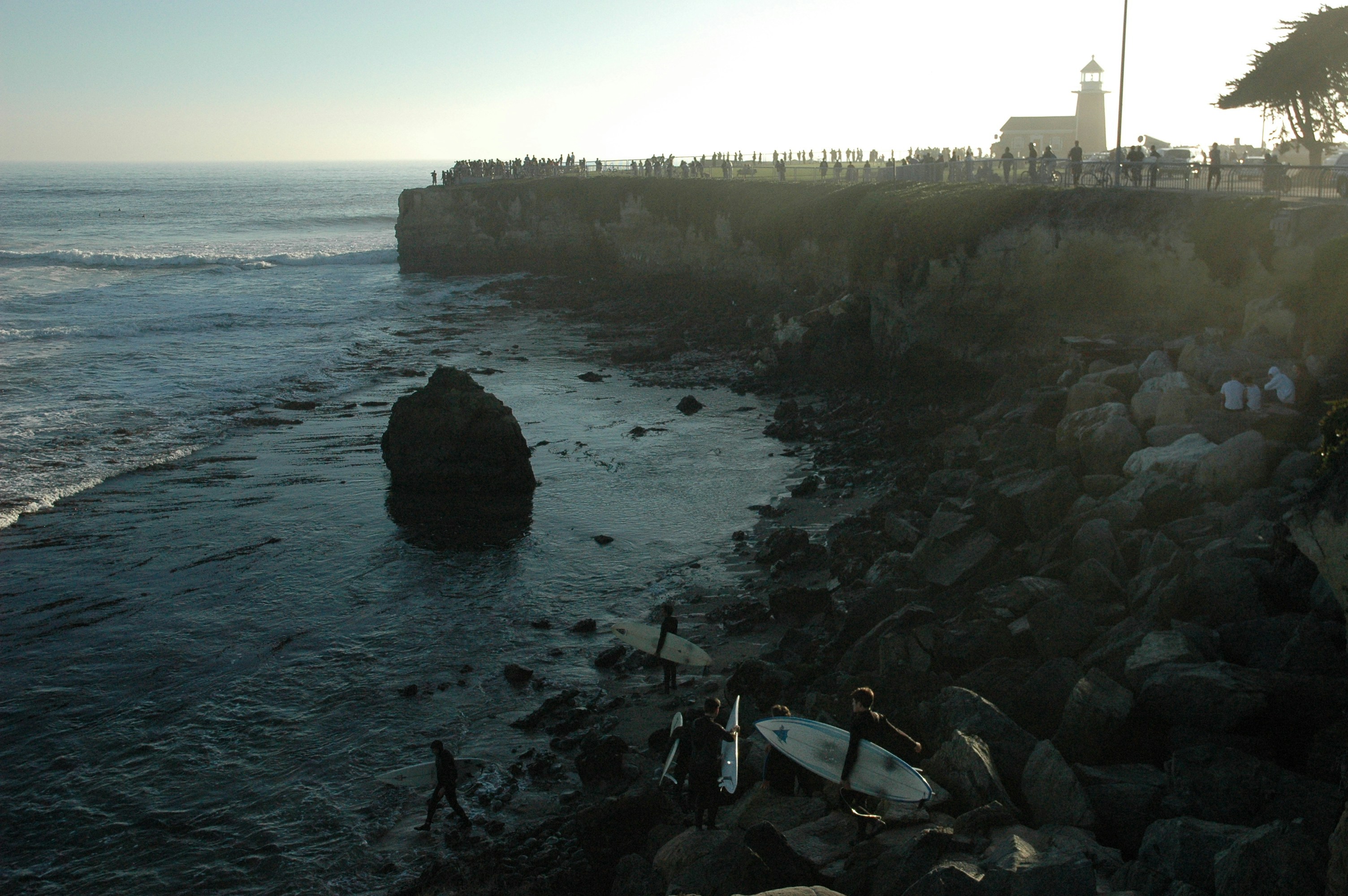Surfers entering the ocean, people enjoying a hot summer day on the Pacific Coast, lighthouse, California  | a group of people standing on top of a cliff next to the ocean