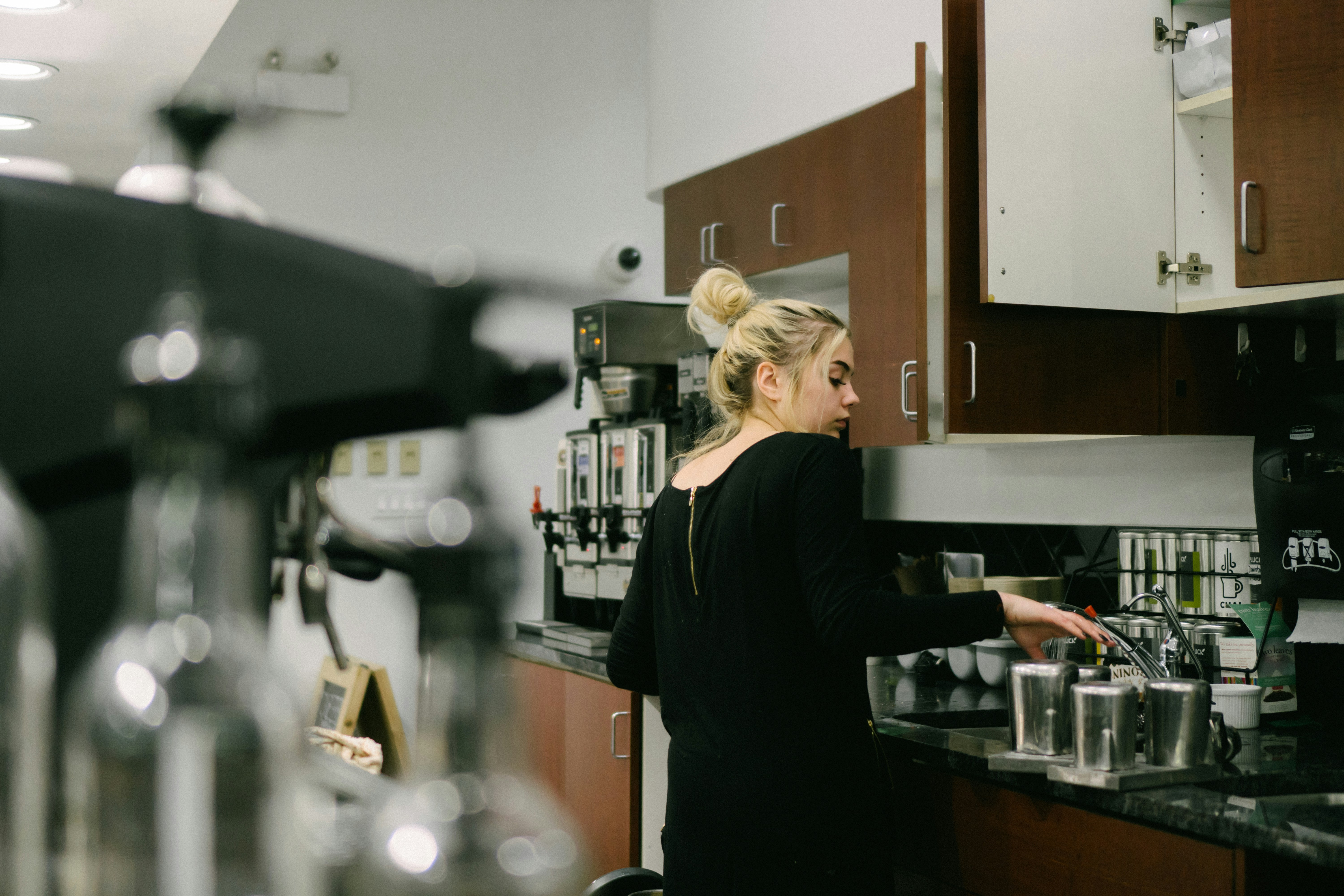 Woman preparing coffee amid sleek kitchen appliances and wooden cabinets.