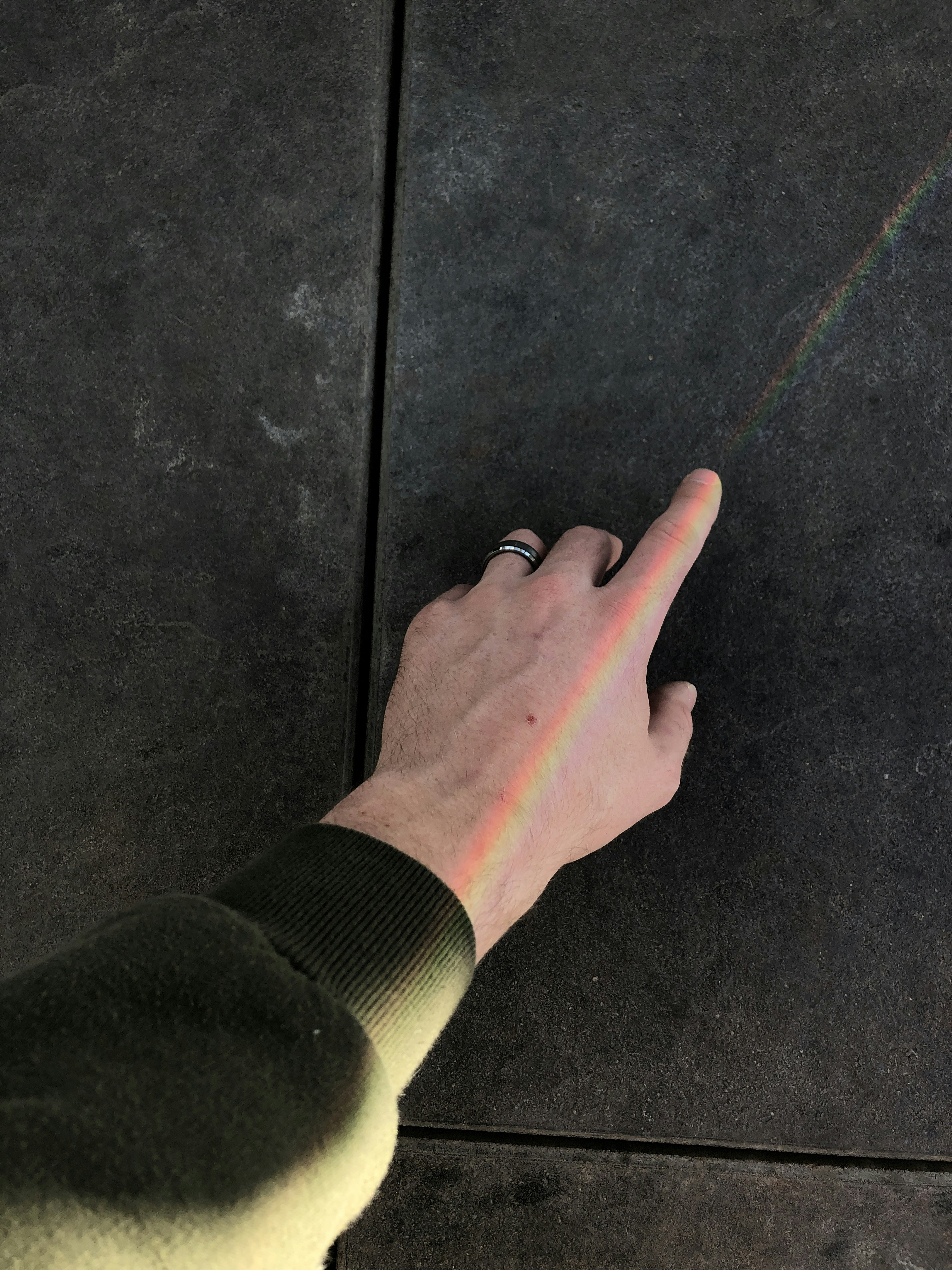A hand extends towards a colorful rainbow reflection on a textured surface, highlighting the interaction between light and human touch.