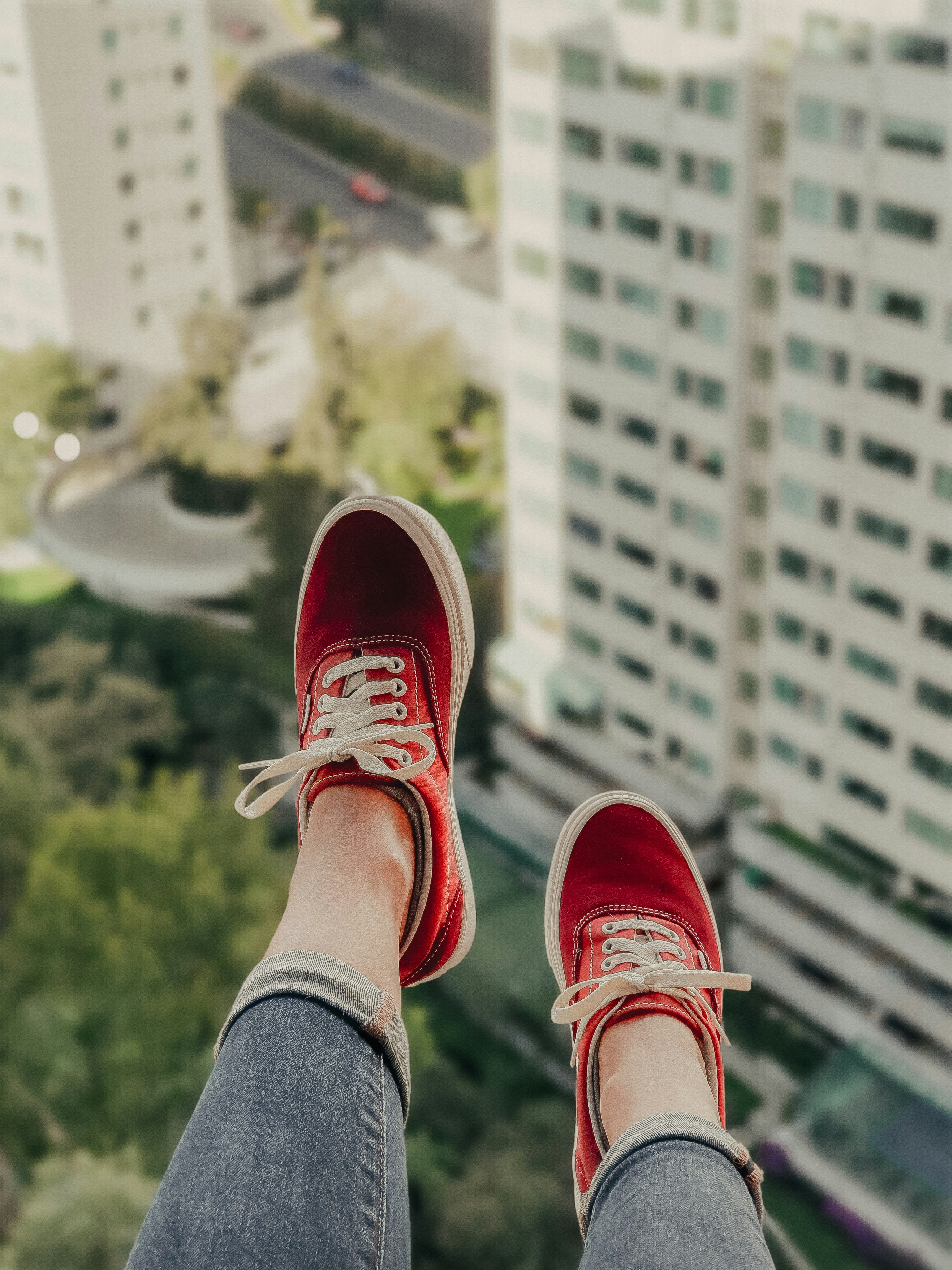 Dangling Red Sneakers Over Cityscape: A Leaning Perspective