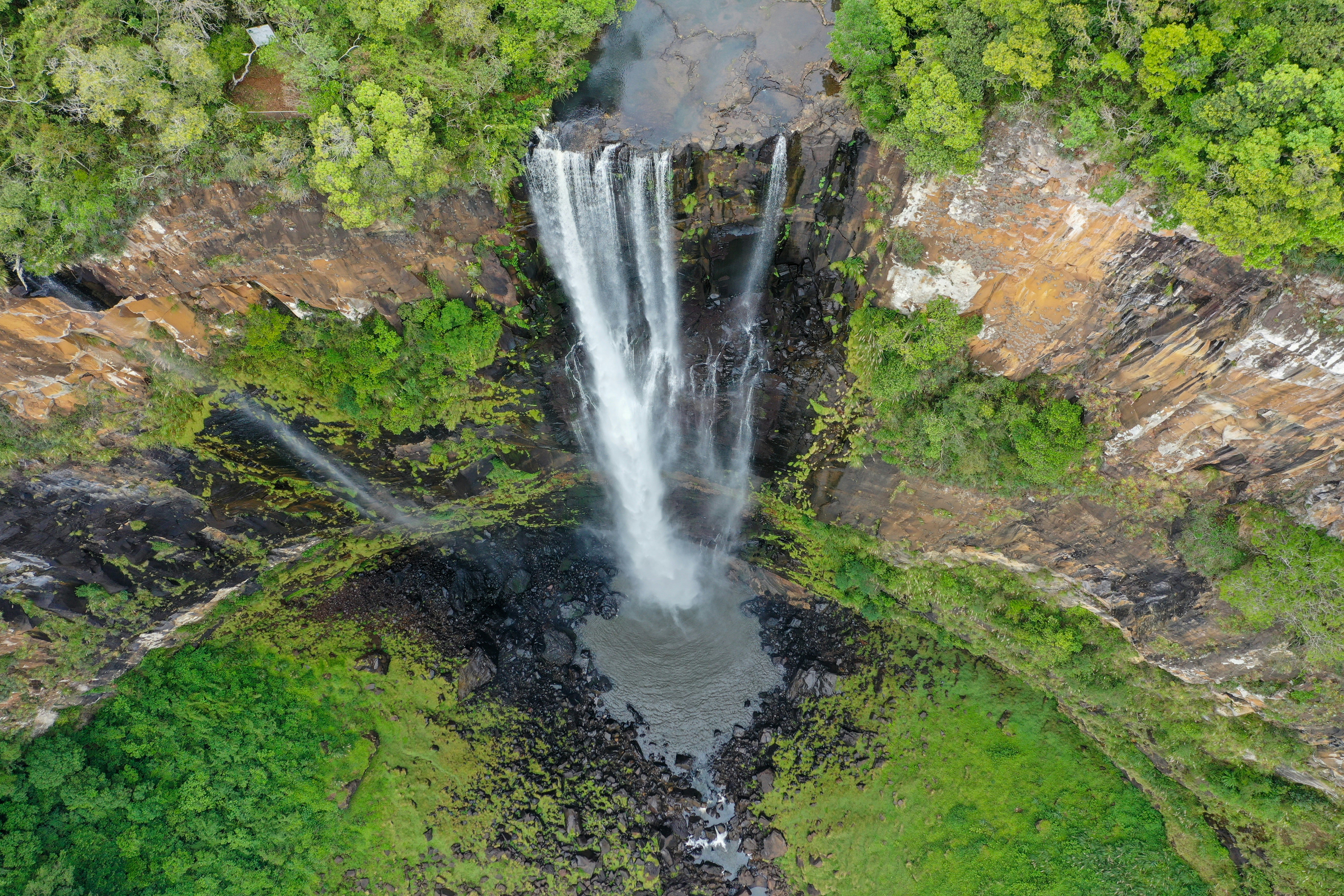 Aerial view of a waterfall surrounded by lush greenery and rocky cliffs during daylight.