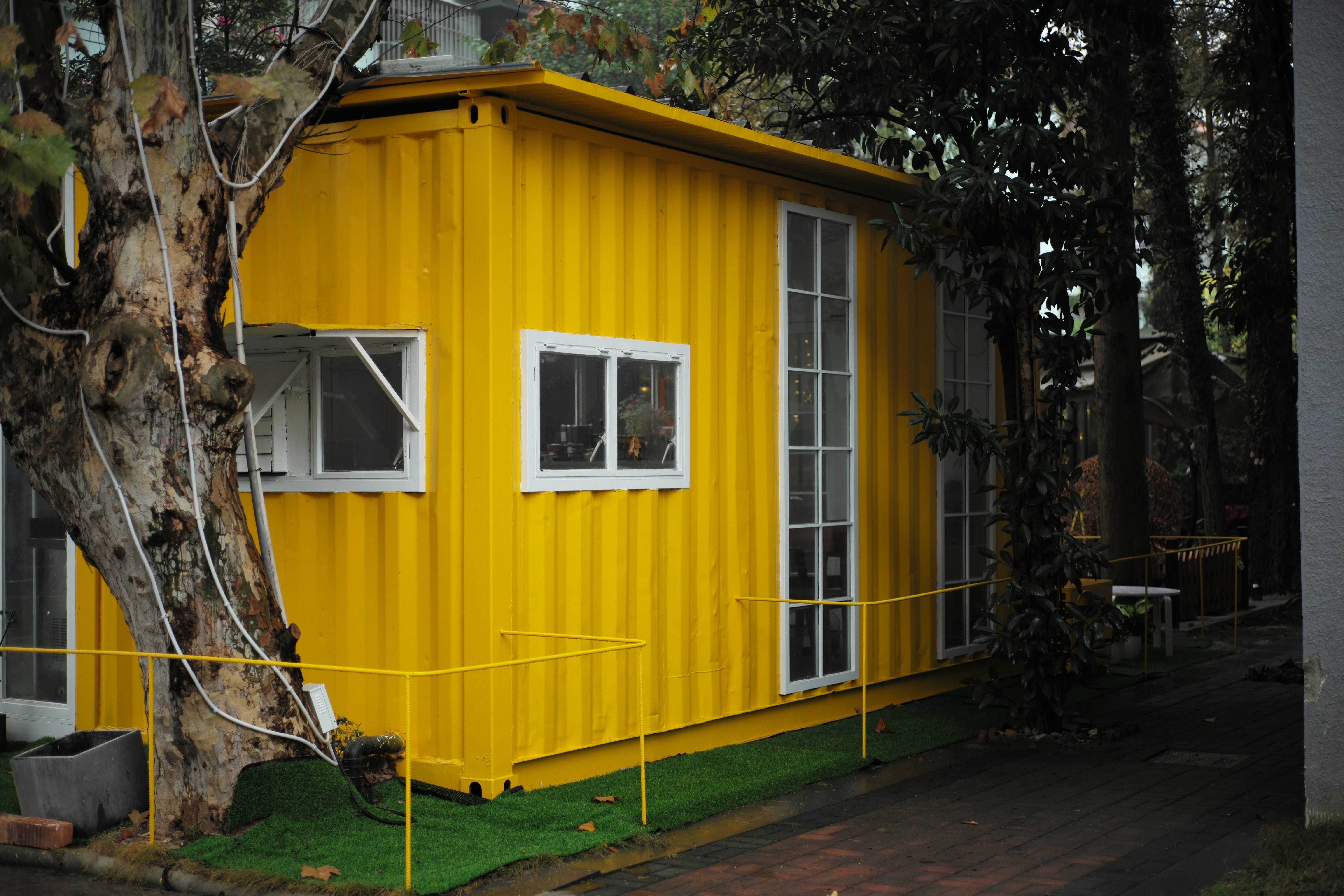 Bright yellow container house nestled among trees, showcasing large windows and a modern design. A blend of industrial and natural elements creates a unique urban retreat.