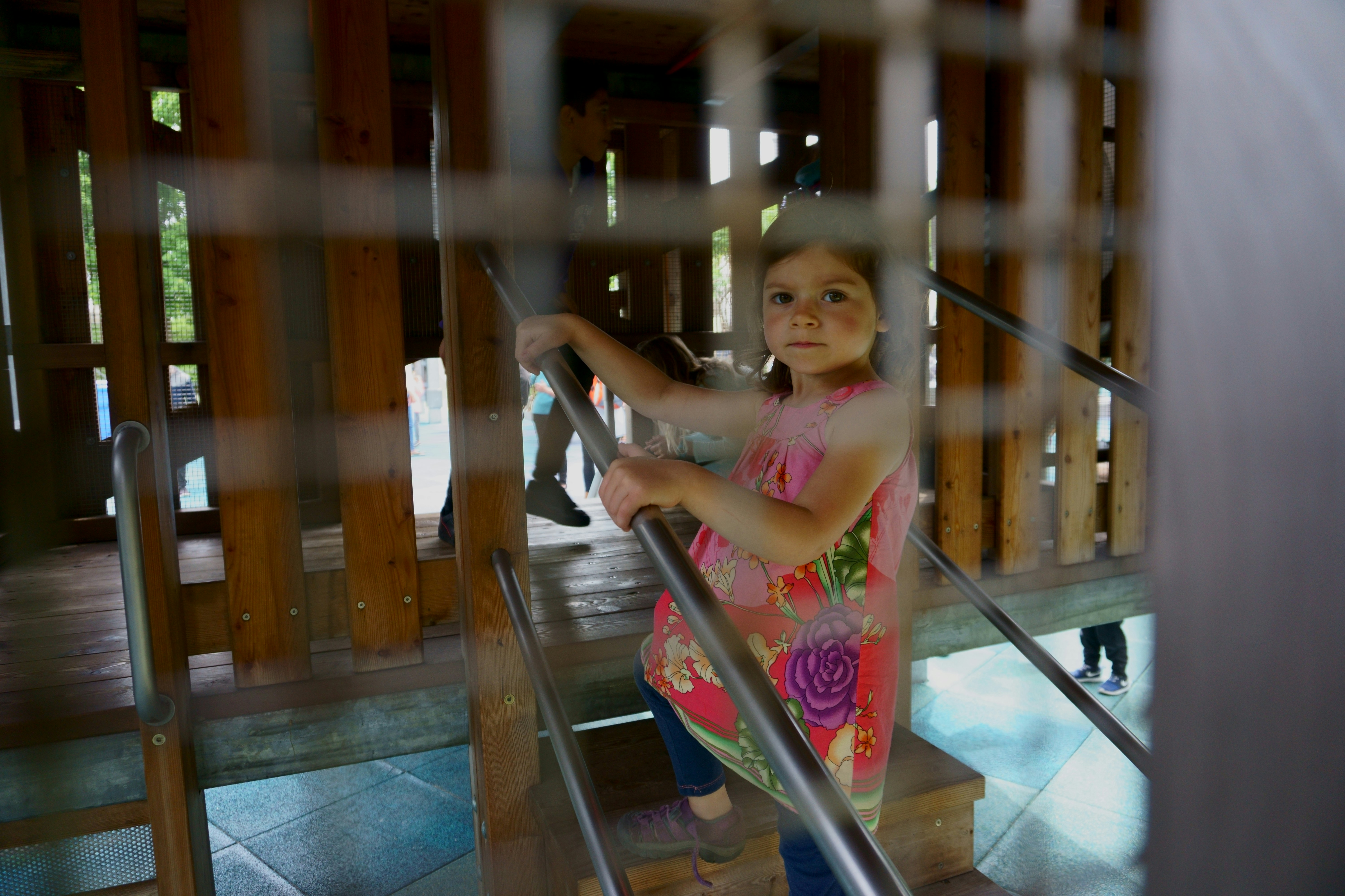 Between Glass and Beams: A Girl Grips the Railing in a Sunlit Timber Pavilion