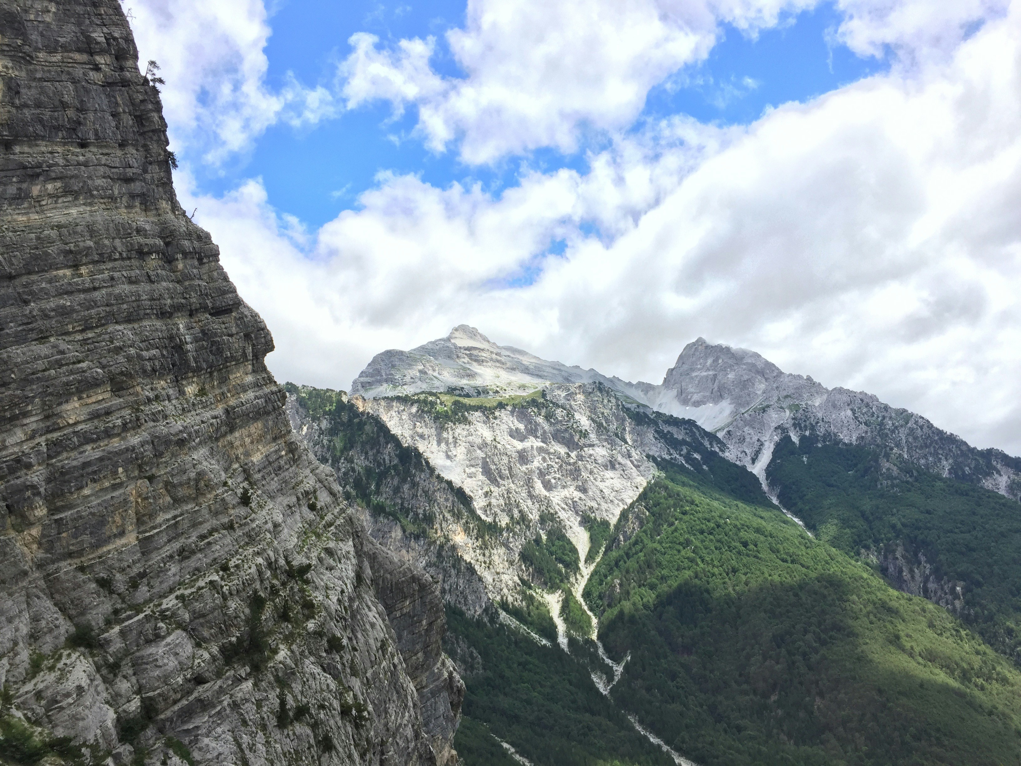 Jagged limestone cliffs rise dramatically against a backdrop of lush green valleys under a partly cloudy sky.