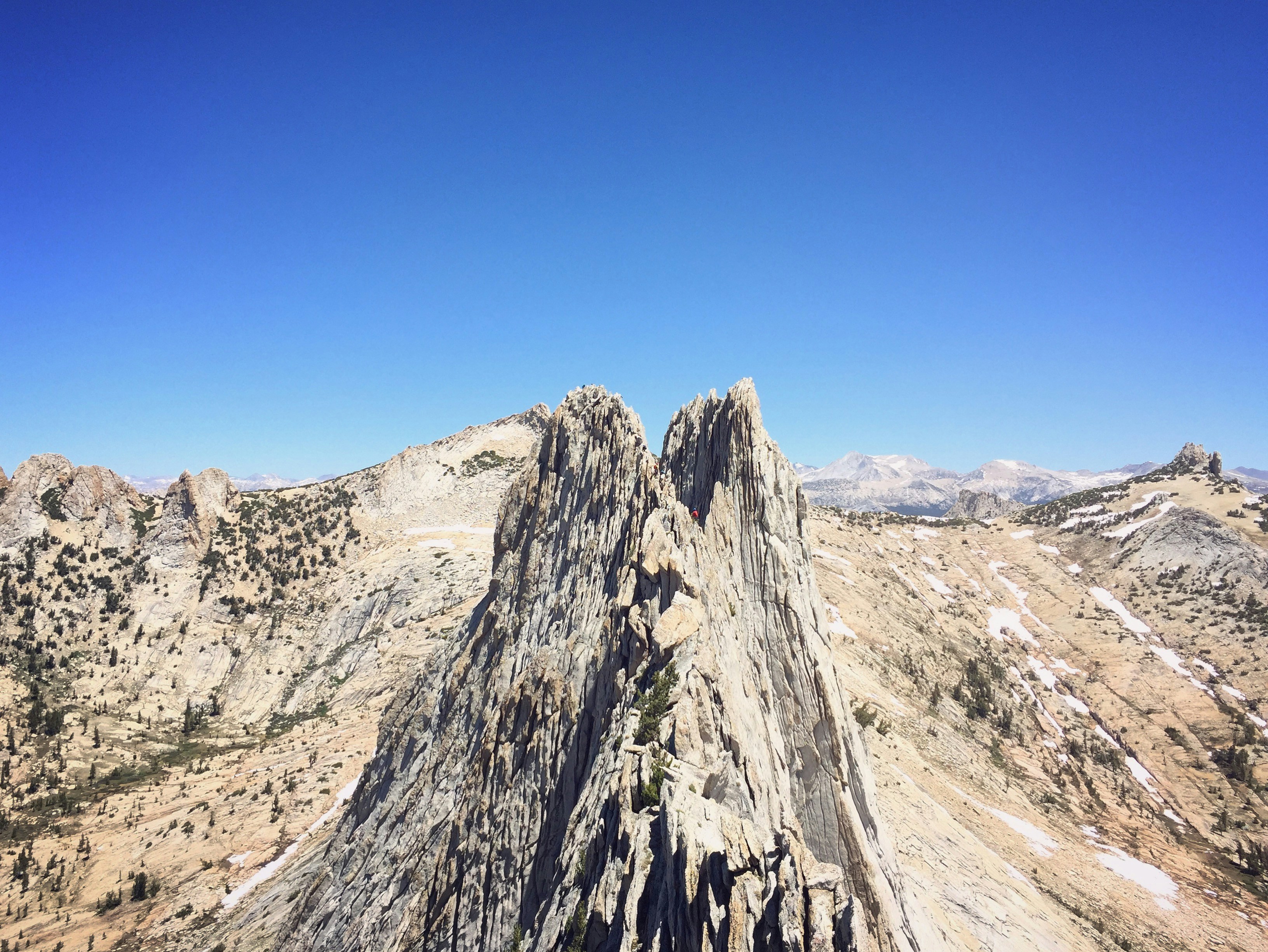 Jagged granite spires rise sharply against a clear blue sky, showcasing the rugged terrain of a mountainous landscape.
