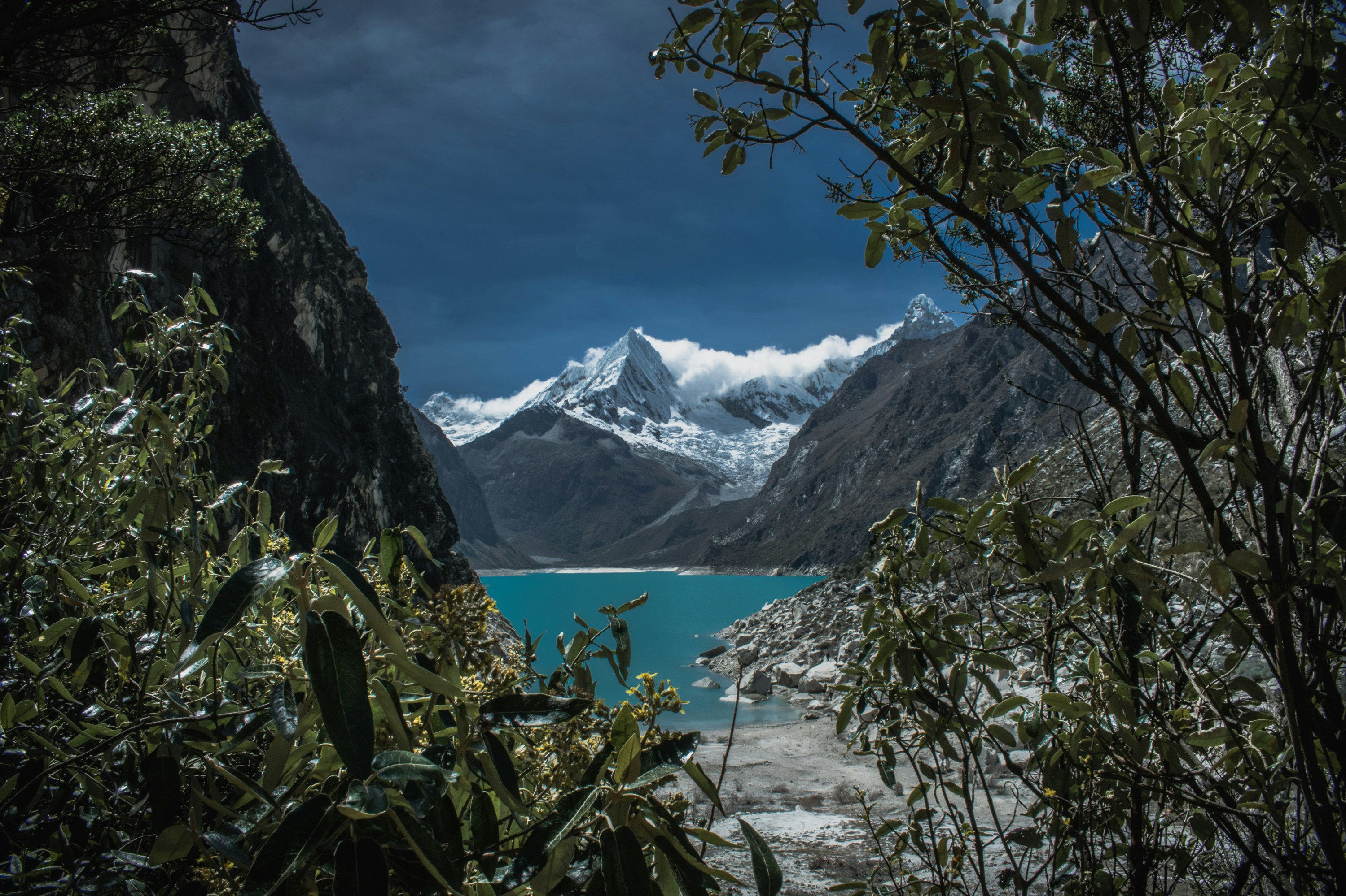 Turquoise Laguna Parón surrounded by towering snow-capped mountains and lush foliage.
