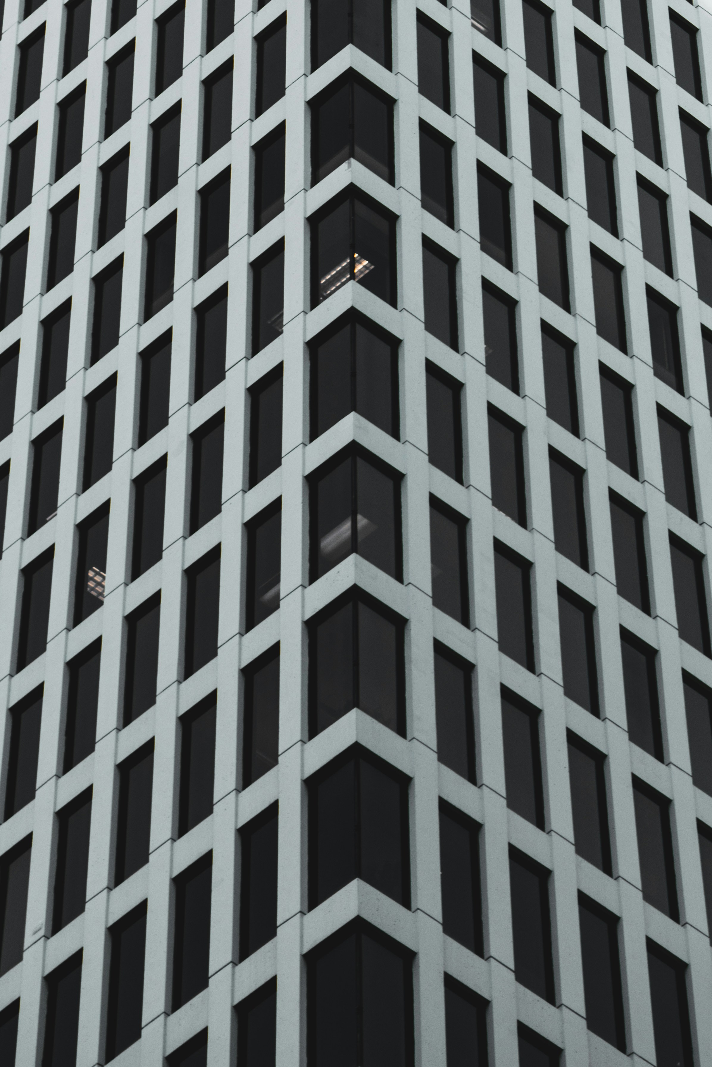 Modern skyscraper facade showcasing a grid of dark windows and angular steel elements. A single illuminated window adds a touch of life to the structure.