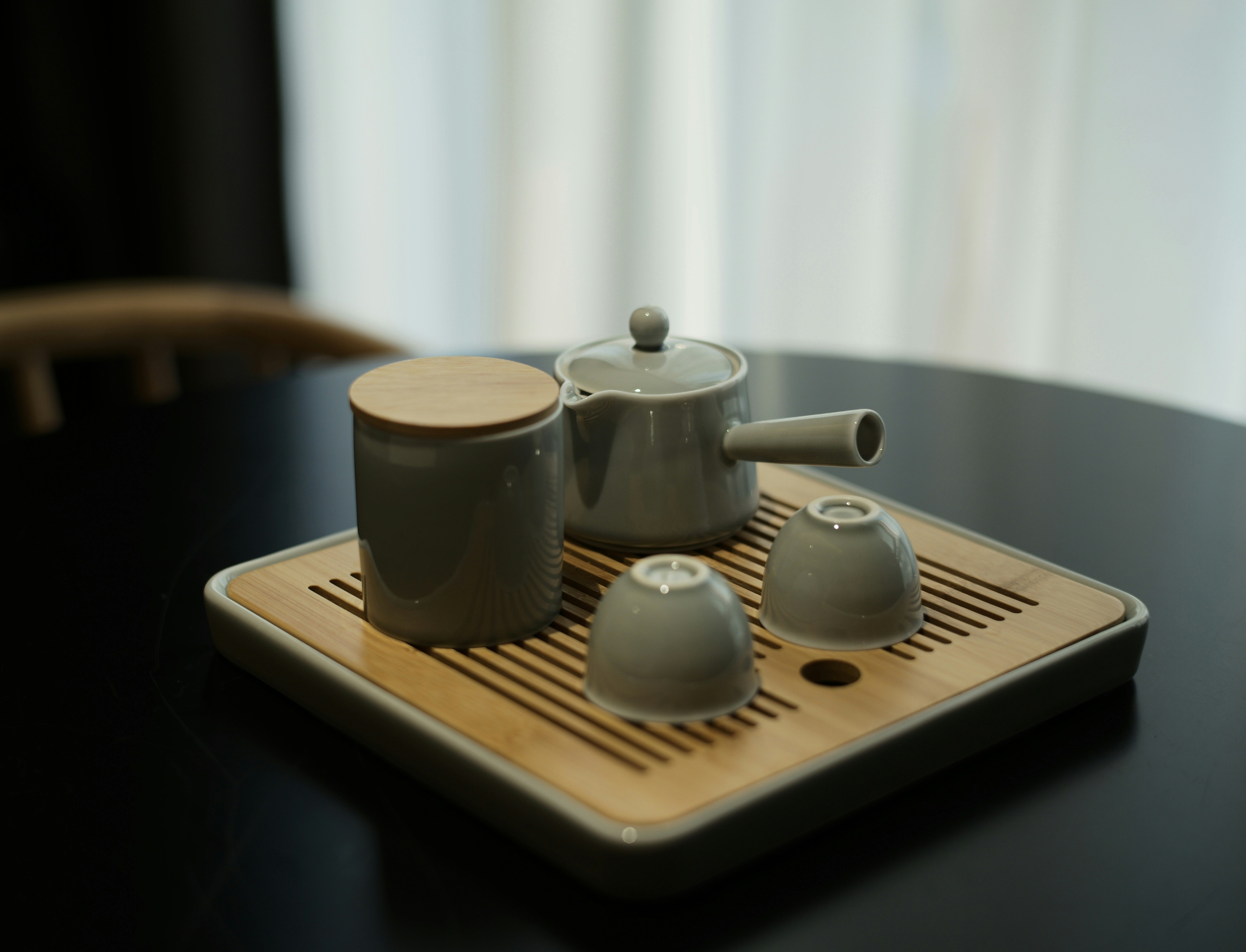 Elegant tea set arranged on a bamboo tray, featuring a teapot, cups, and a covered container. Soft natural light enhances the tranquil atmosphere.