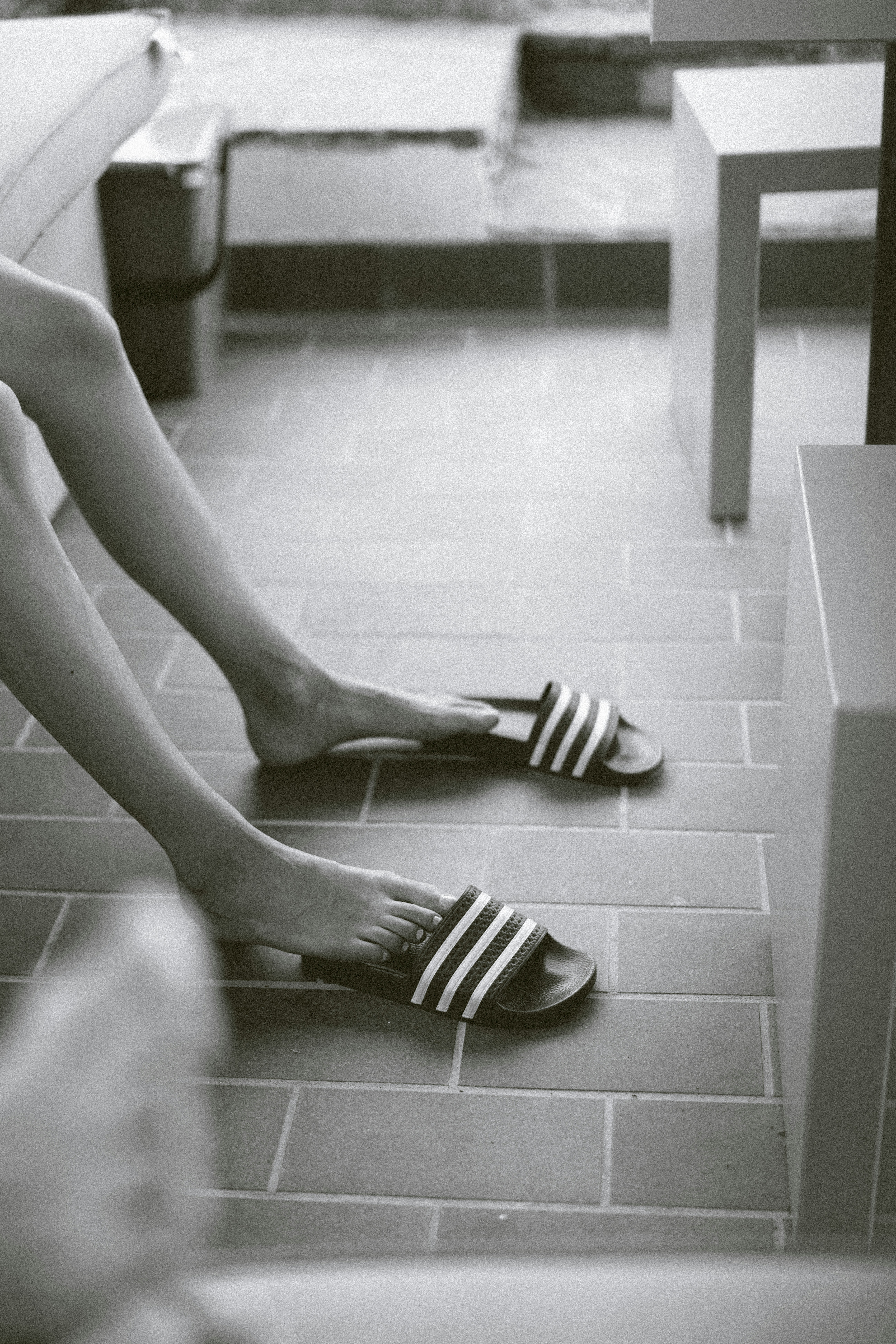 A pair of feet in black and white slide sandals resting on tiled flooring, conveying a sense of relaxation and casual living.