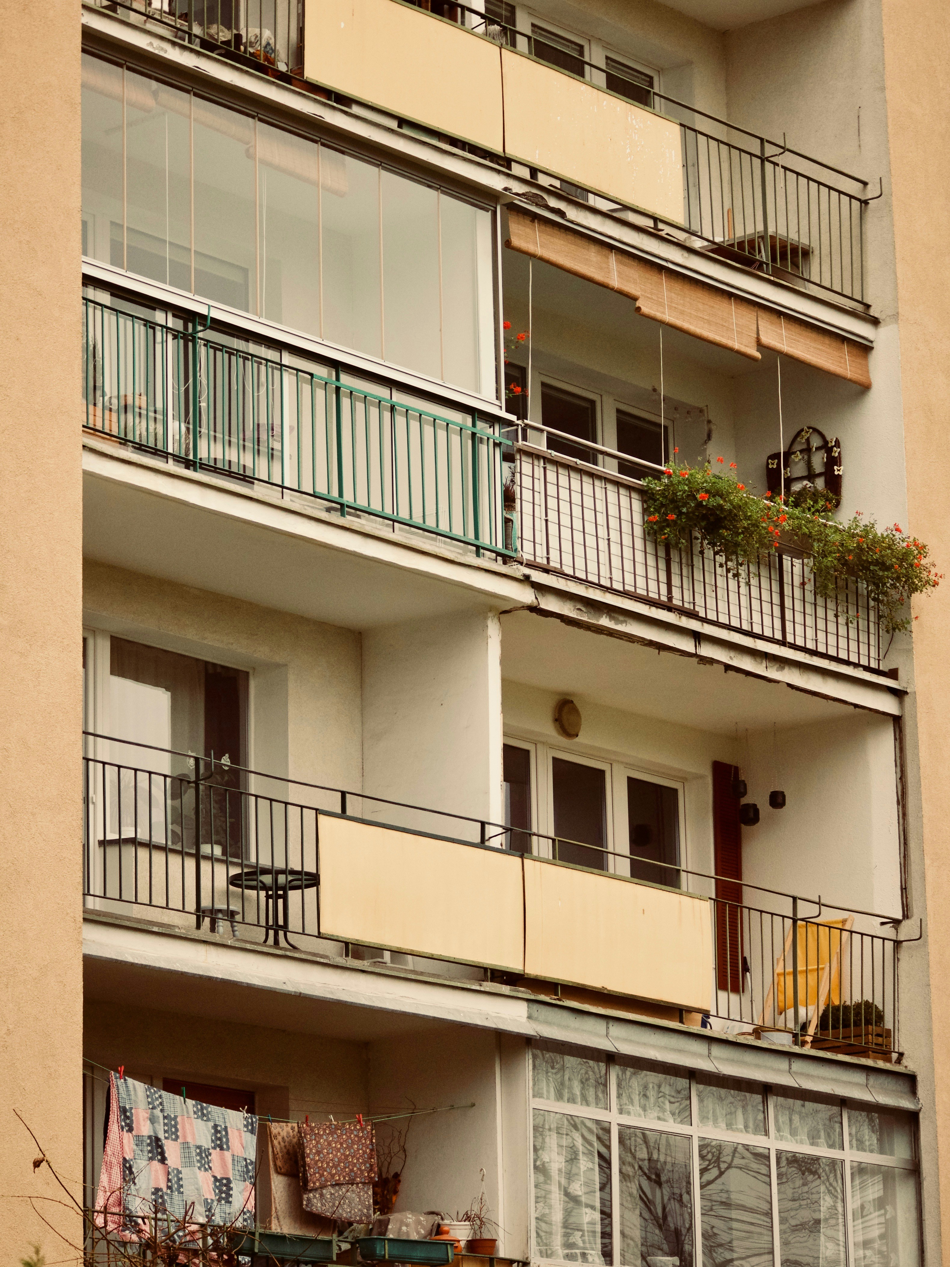 Three balconies adorned with plants and personal items, showcasing urban living. The scene captures the essence of home in a city environment.