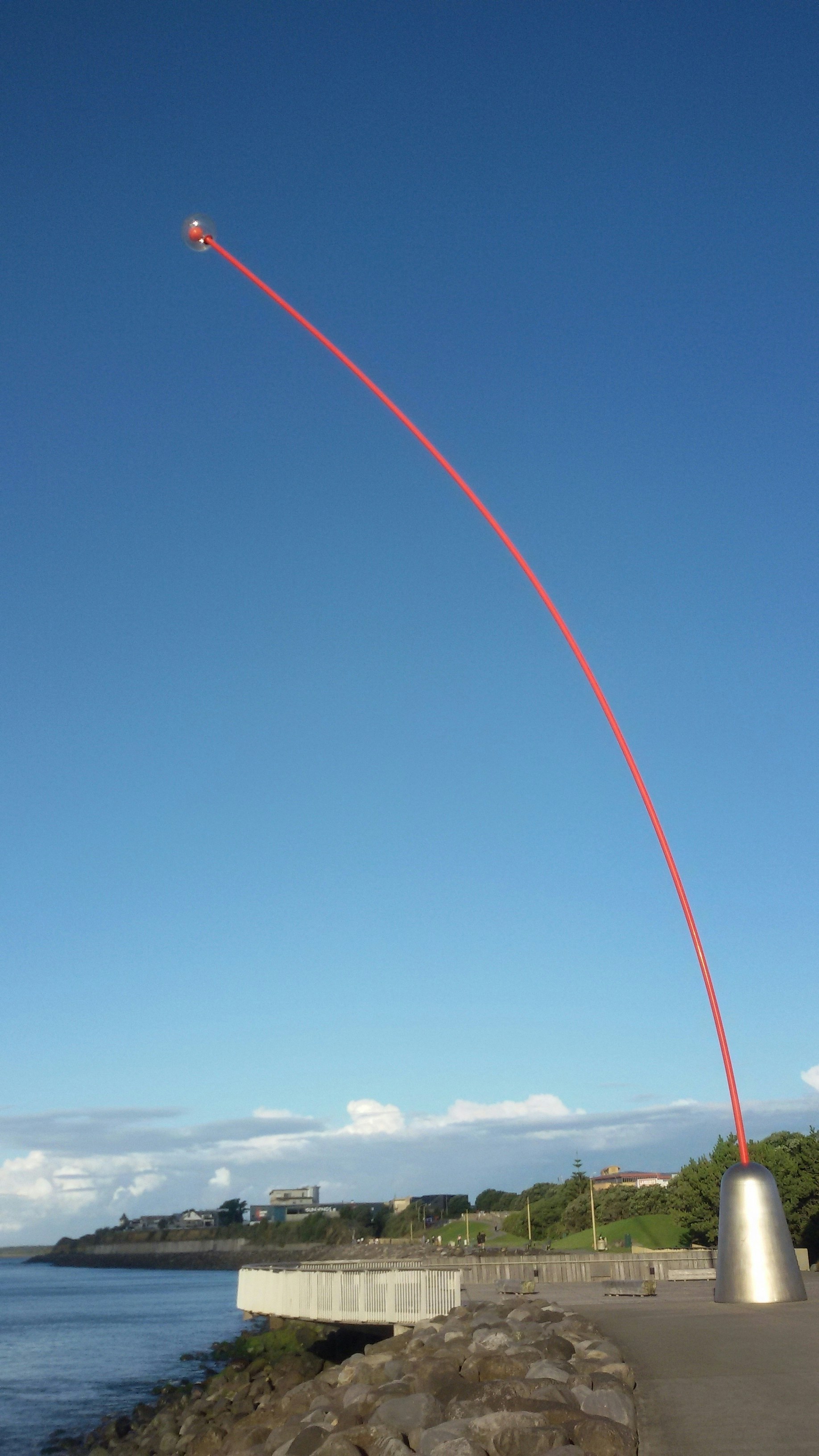 Red Ribbon Arches Over the Sea: A Coastal Sculpture in Motion