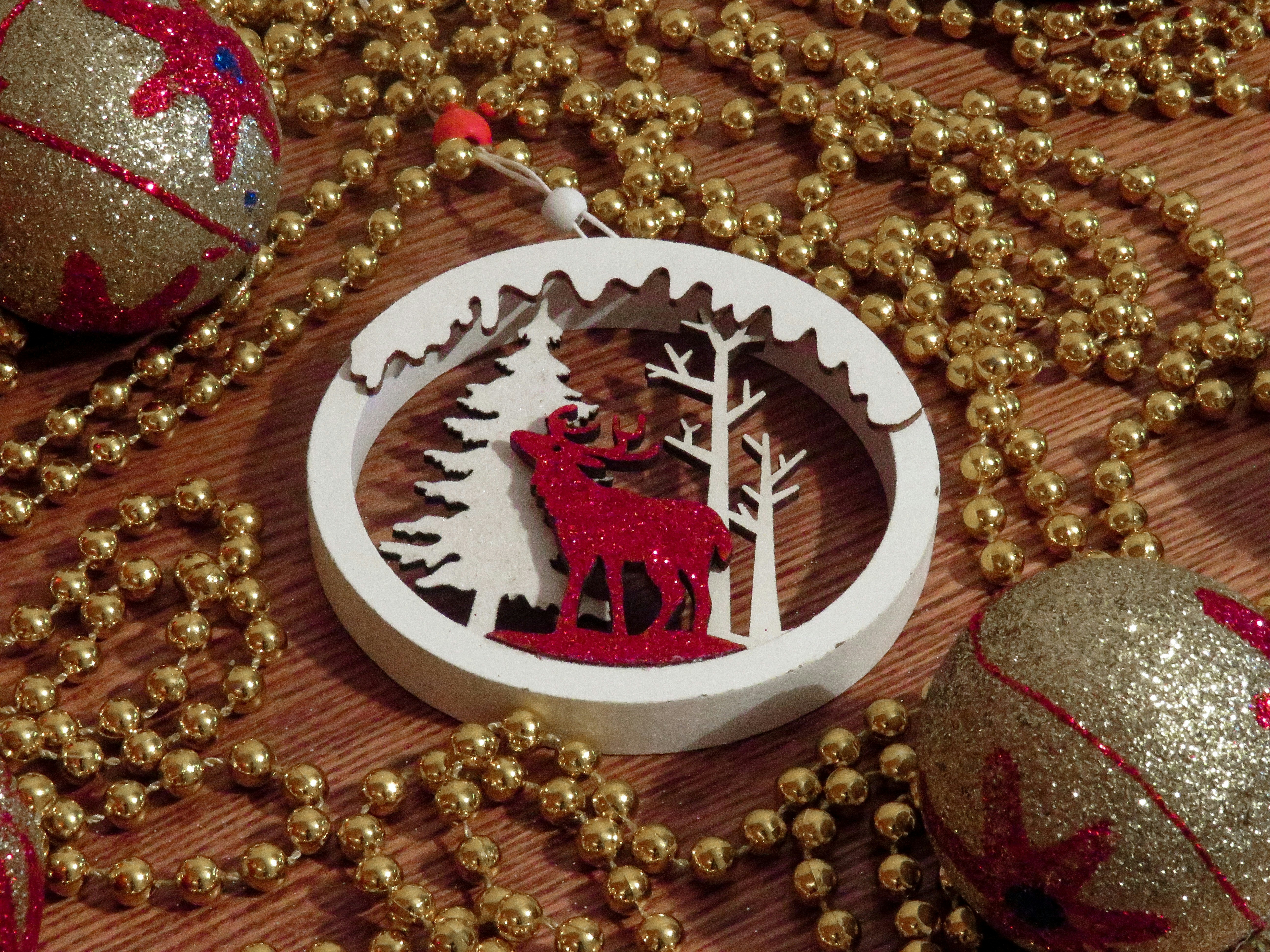 Decorative ornament featuring a reindeer and trees, surrounded by golden beads and Christmas baubles.