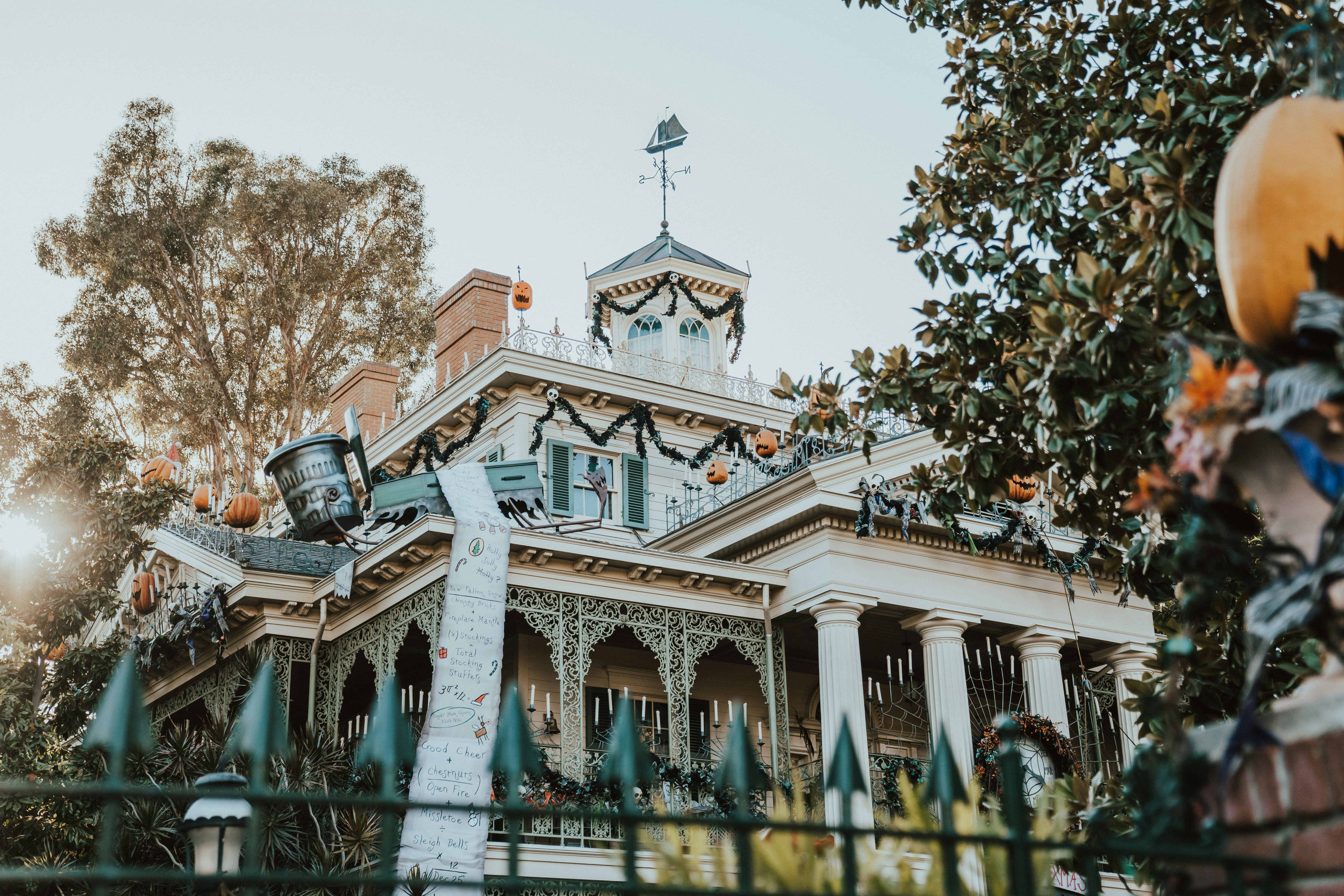 Victorian-style mansion decorated with Halloween ornaments and surrounded by lush trees.