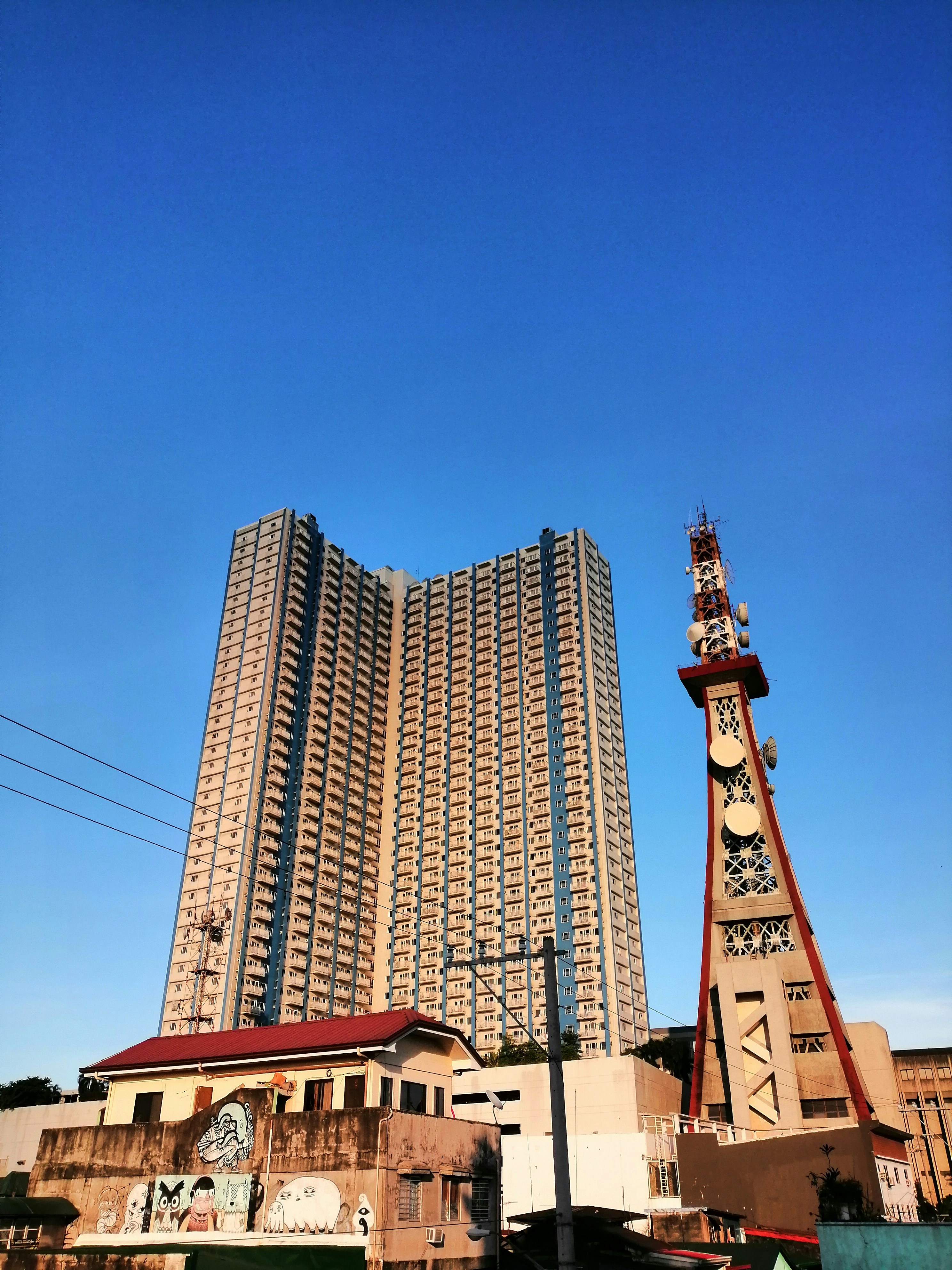 Tall concrete high-rise and a red-and-beige communications tower rise against a clear blue sky.