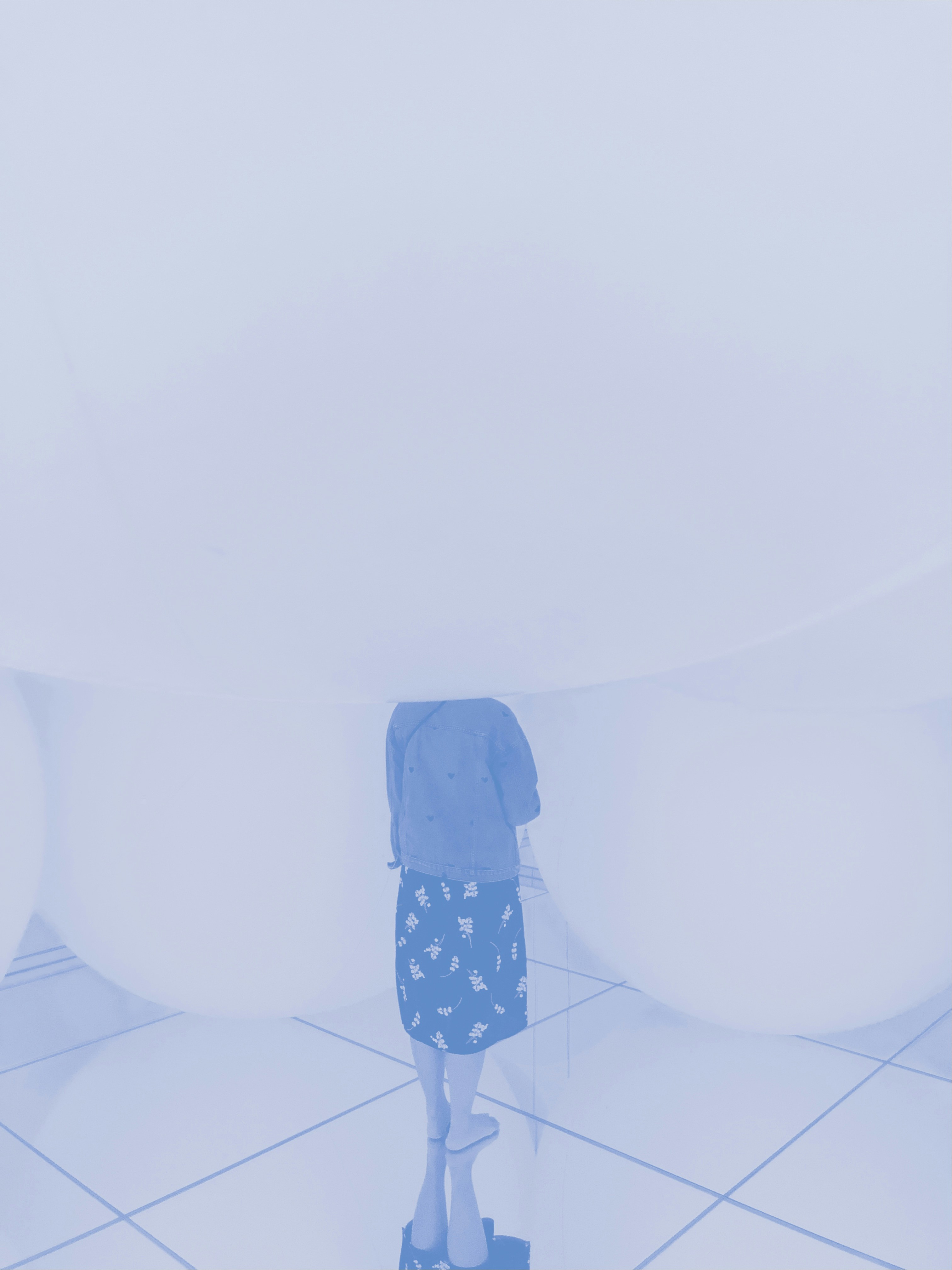 A figure partially obscured by large white spheres, exploring a minimalist space that evokes a sense of wonder and introspection.