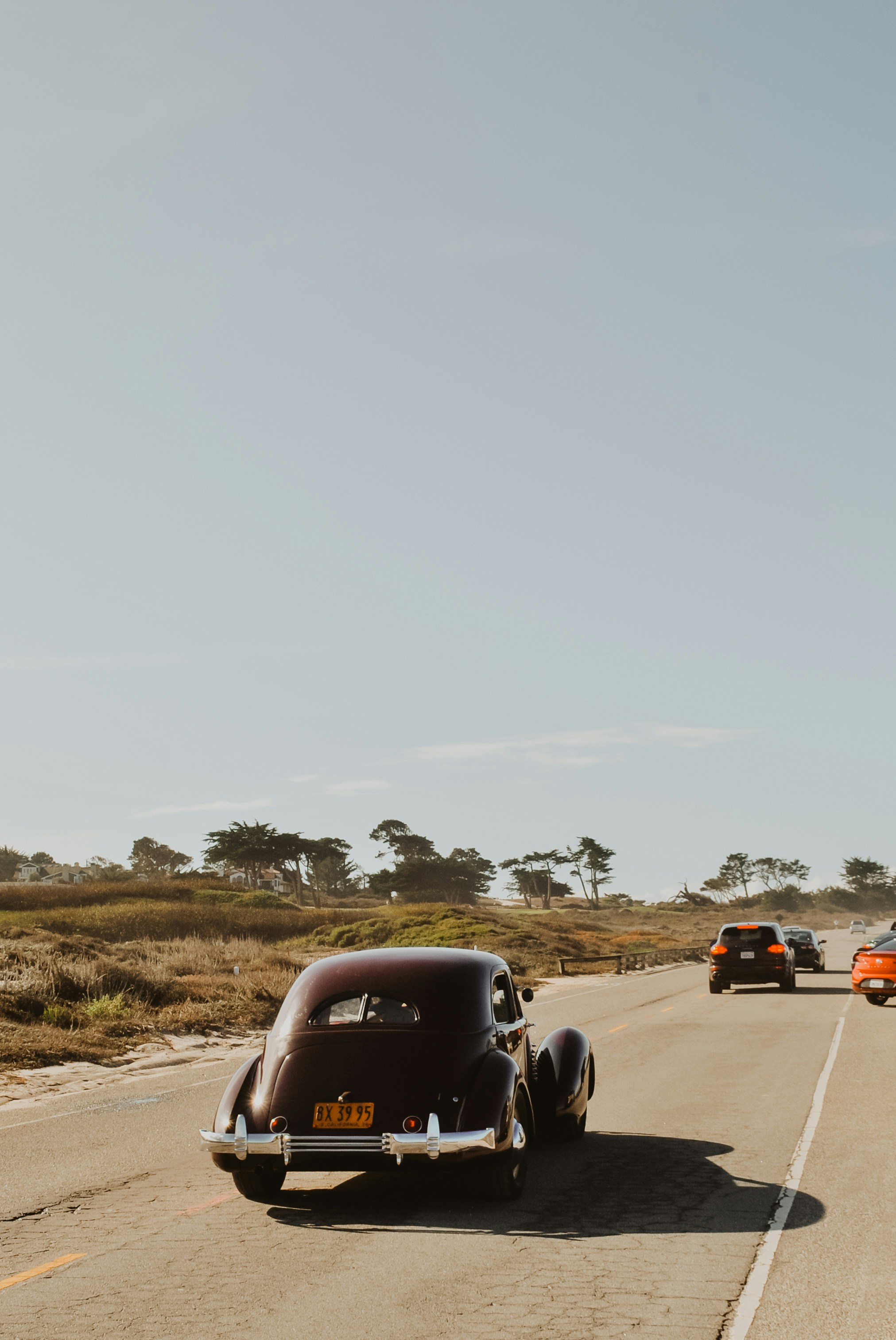 Classic car driving along a coastal road, surrounded by scenic landscapes and clear skies.