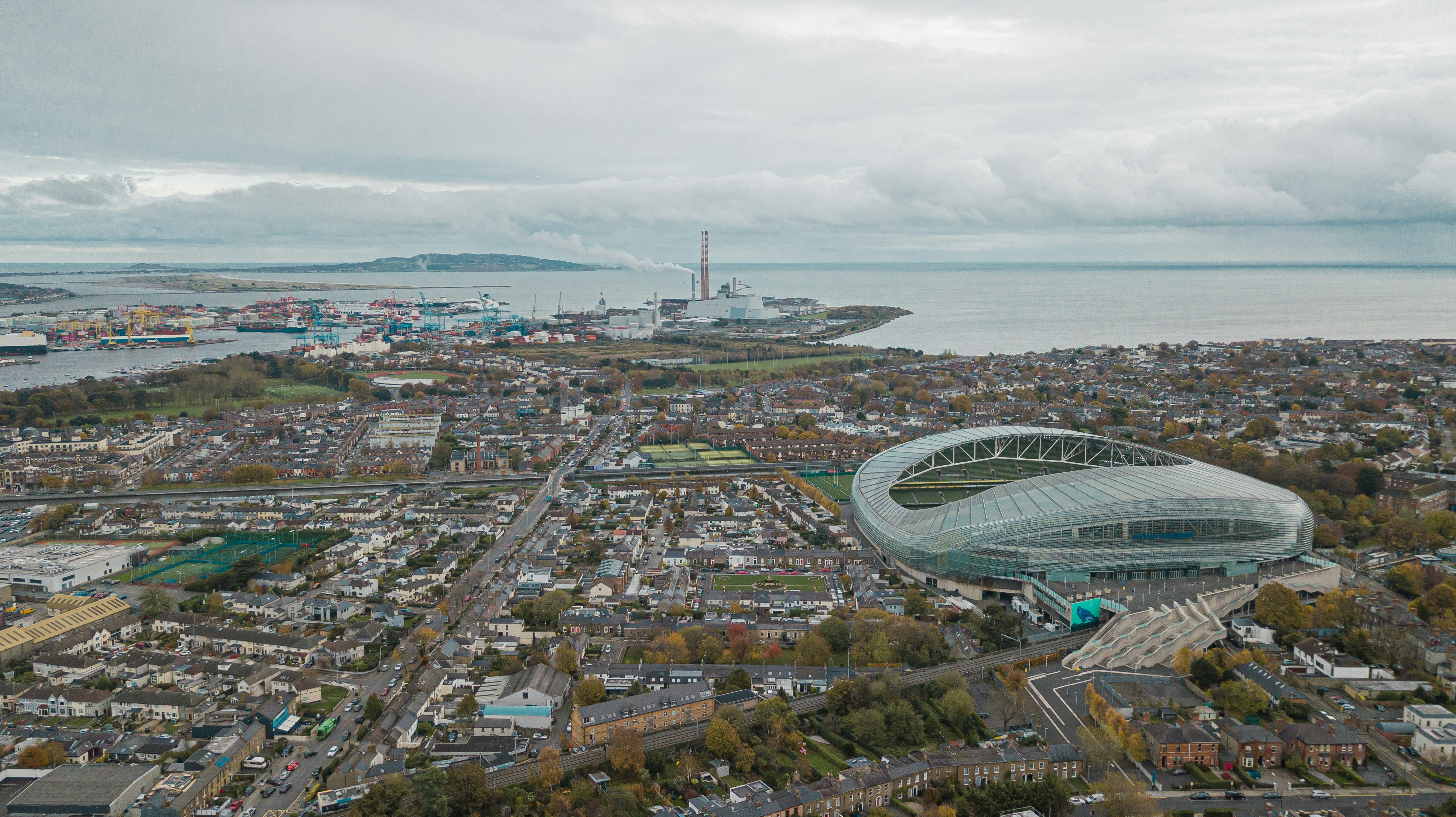 Aerial view of a coastal city with a distinctive oval stadium and expansive waterfront.