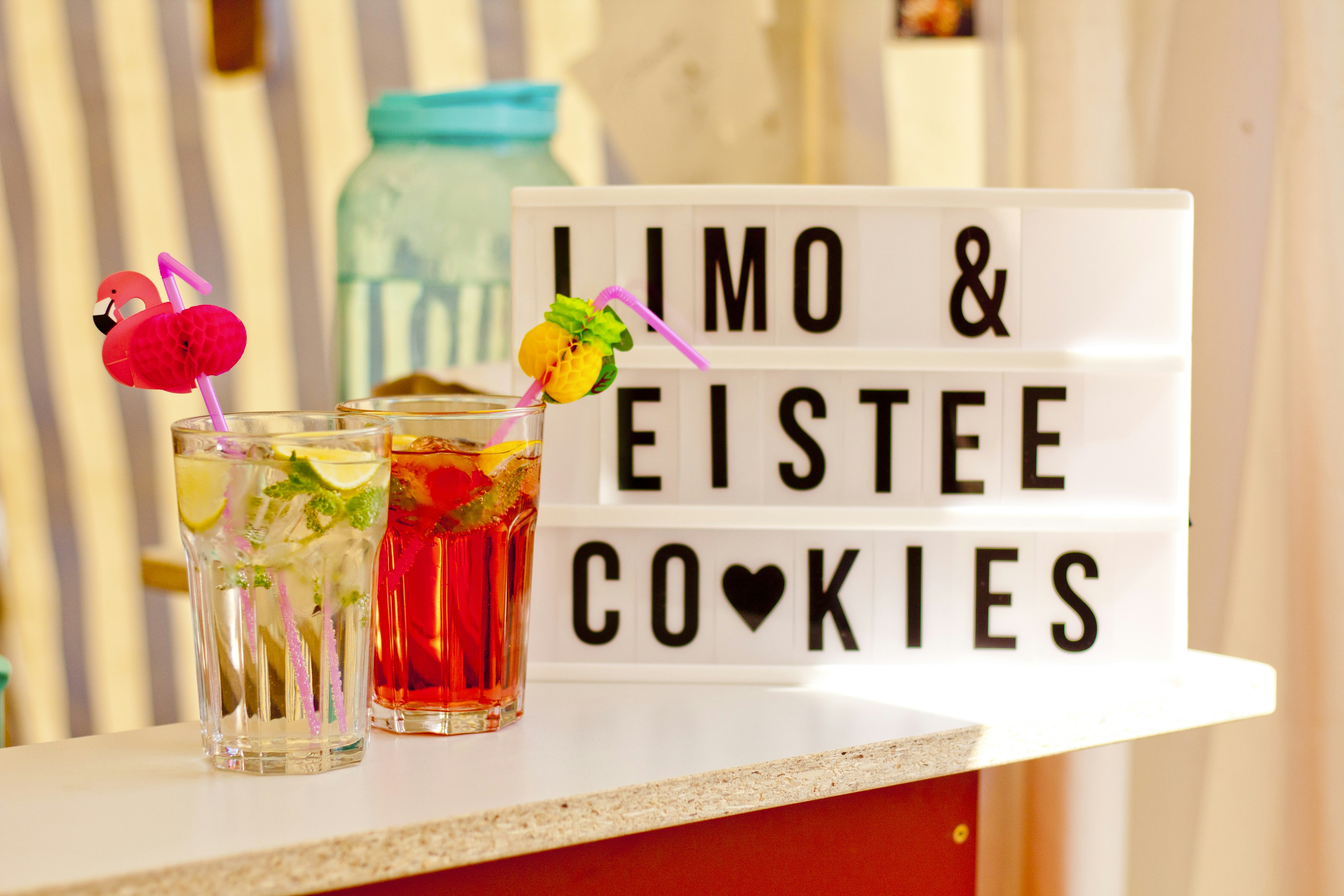 Sunlit Countertop Duo: Mint Mojito and Crimson Iced Tea by a Cookies Sign