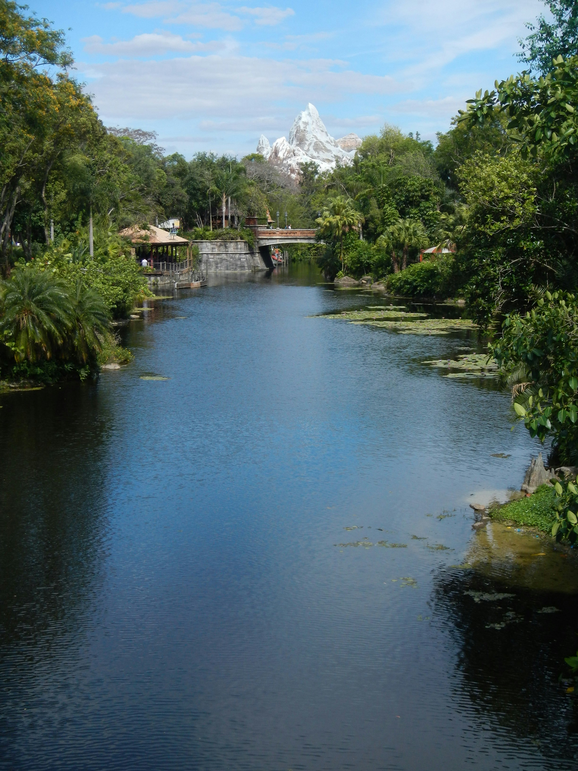 A tranquil river flows through lush greenery, with the iconic snowy peak of a mountain visible in the background. The scene captures the harmony of nature and design.