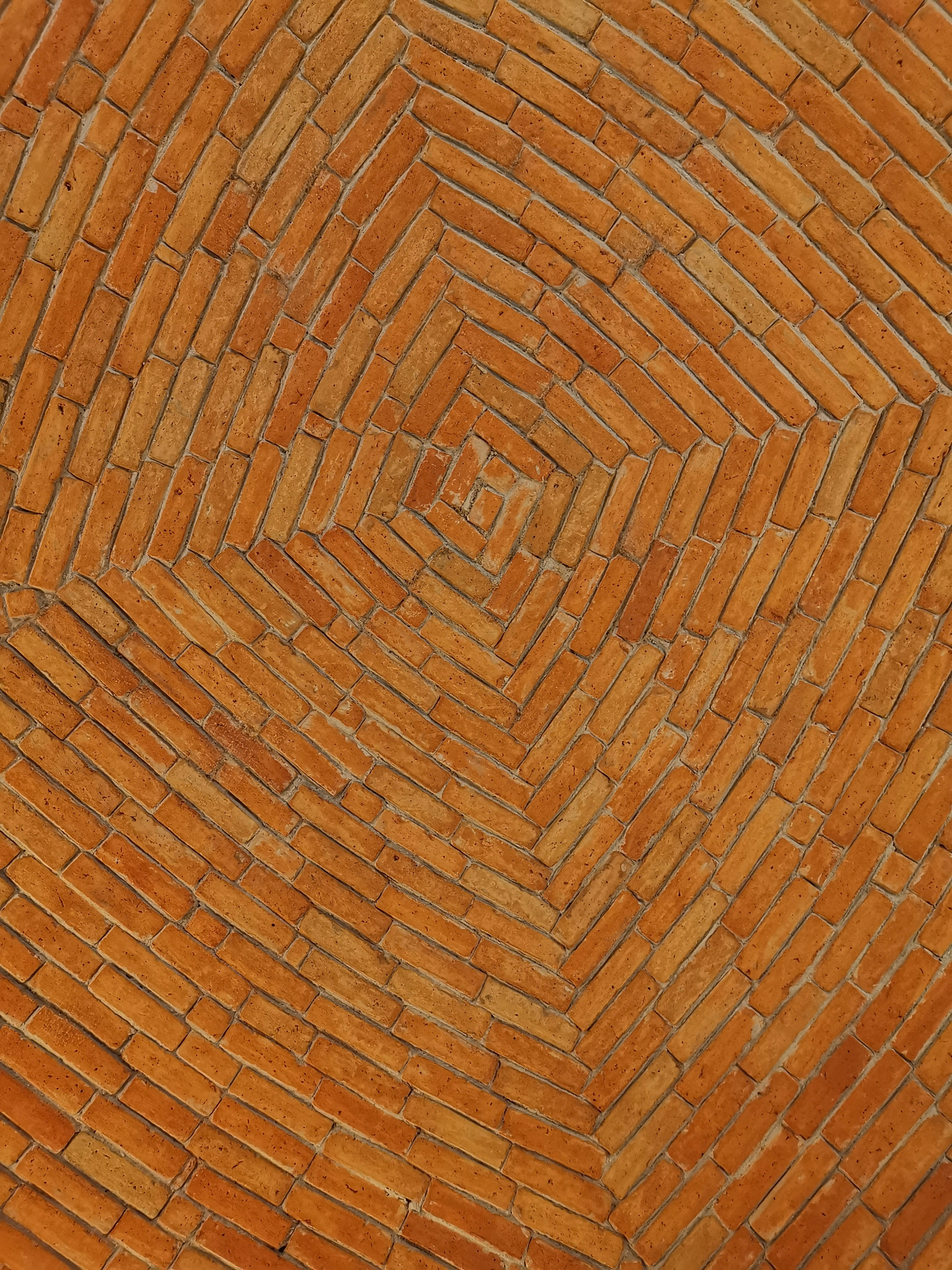 Terracotta brick wall with a concentric herringbone spiral that draws the eye to the center.