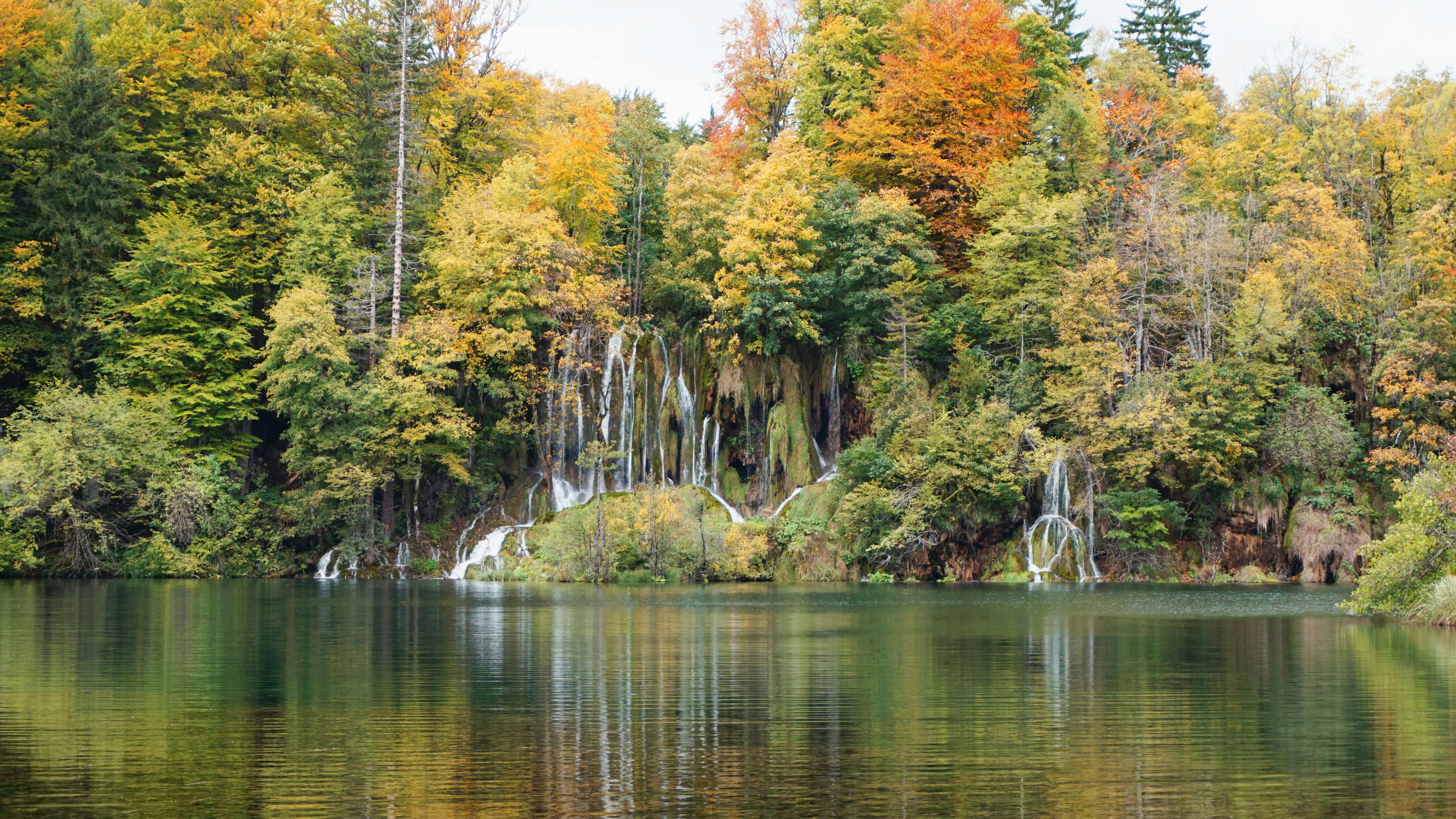 Colorful autumn foliage surrounds cascading waterfalls reflecting in a tranquil lake.